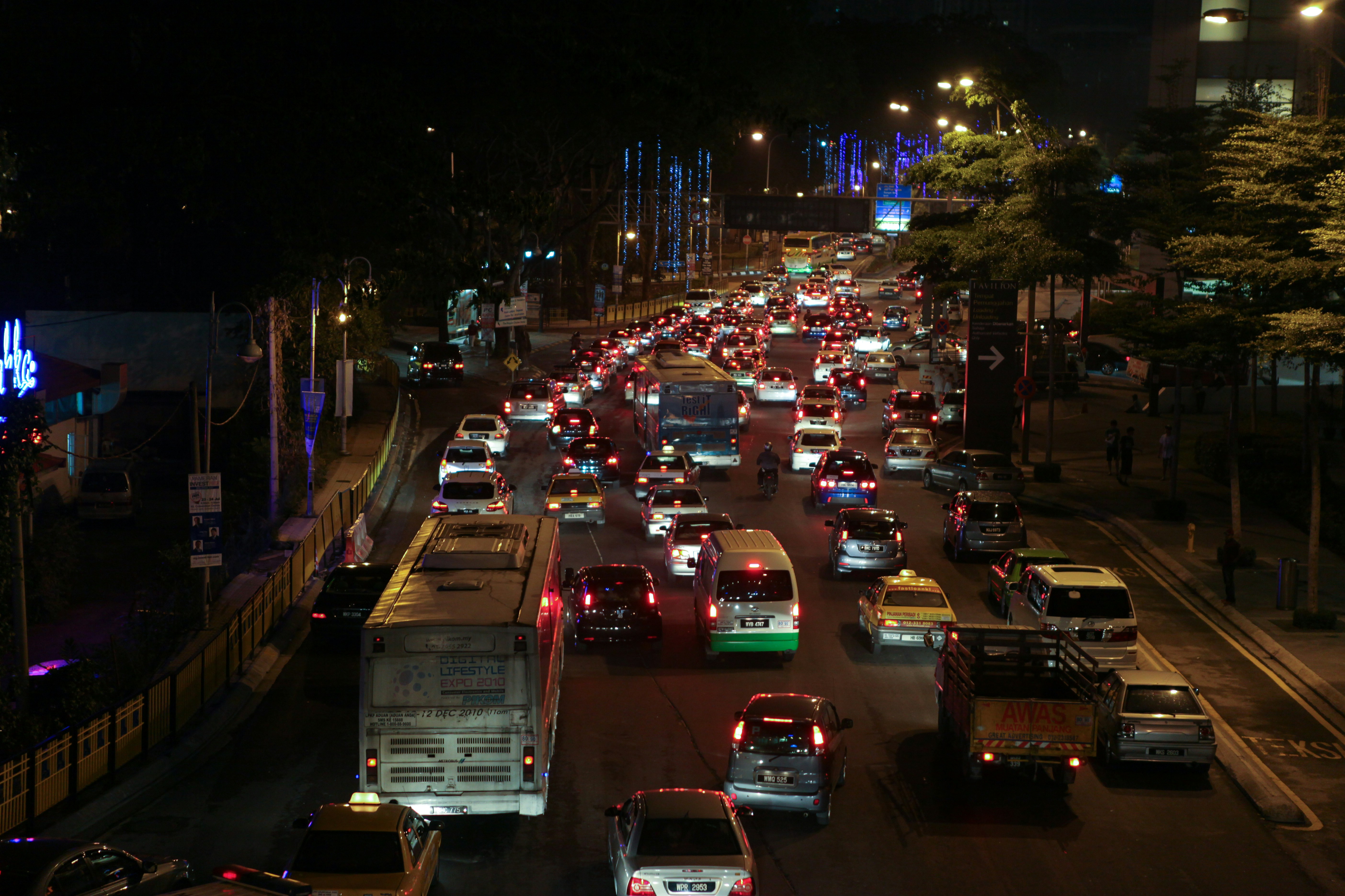 Busy city street filled with a mix of vehicles during nighttime, illuminated by city lights and traffic signals.