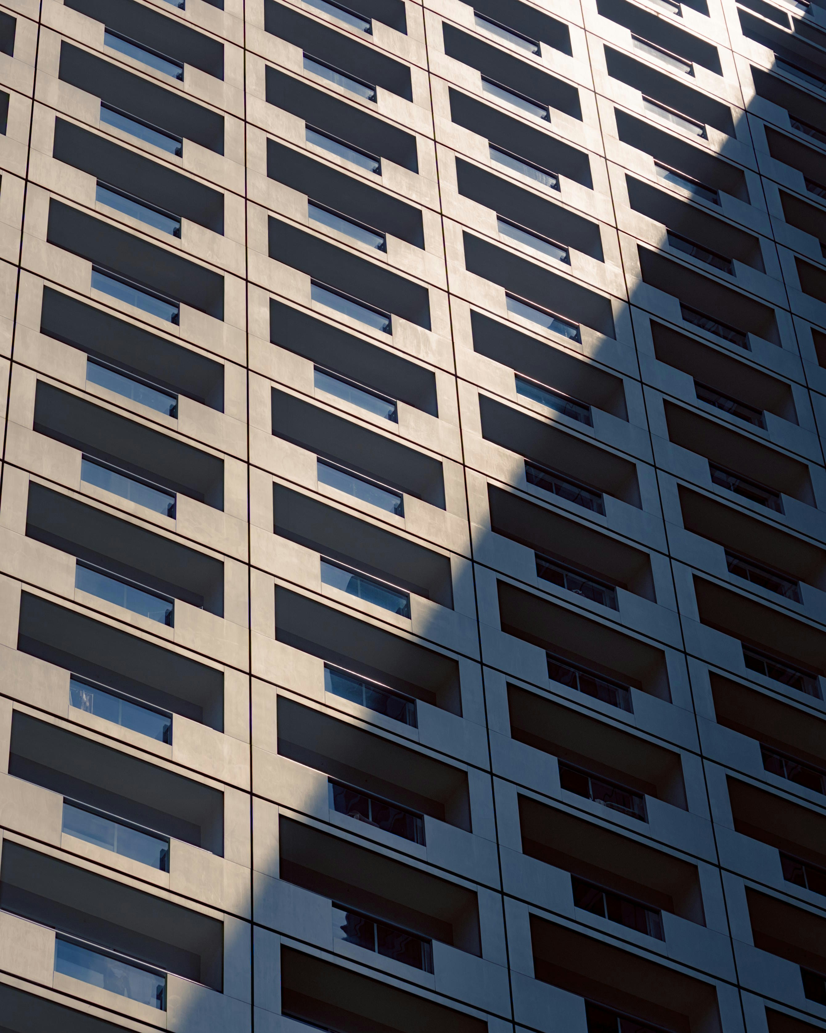 Abstract view of a modern building facade with geometric patterns and shadows created by sunlight.