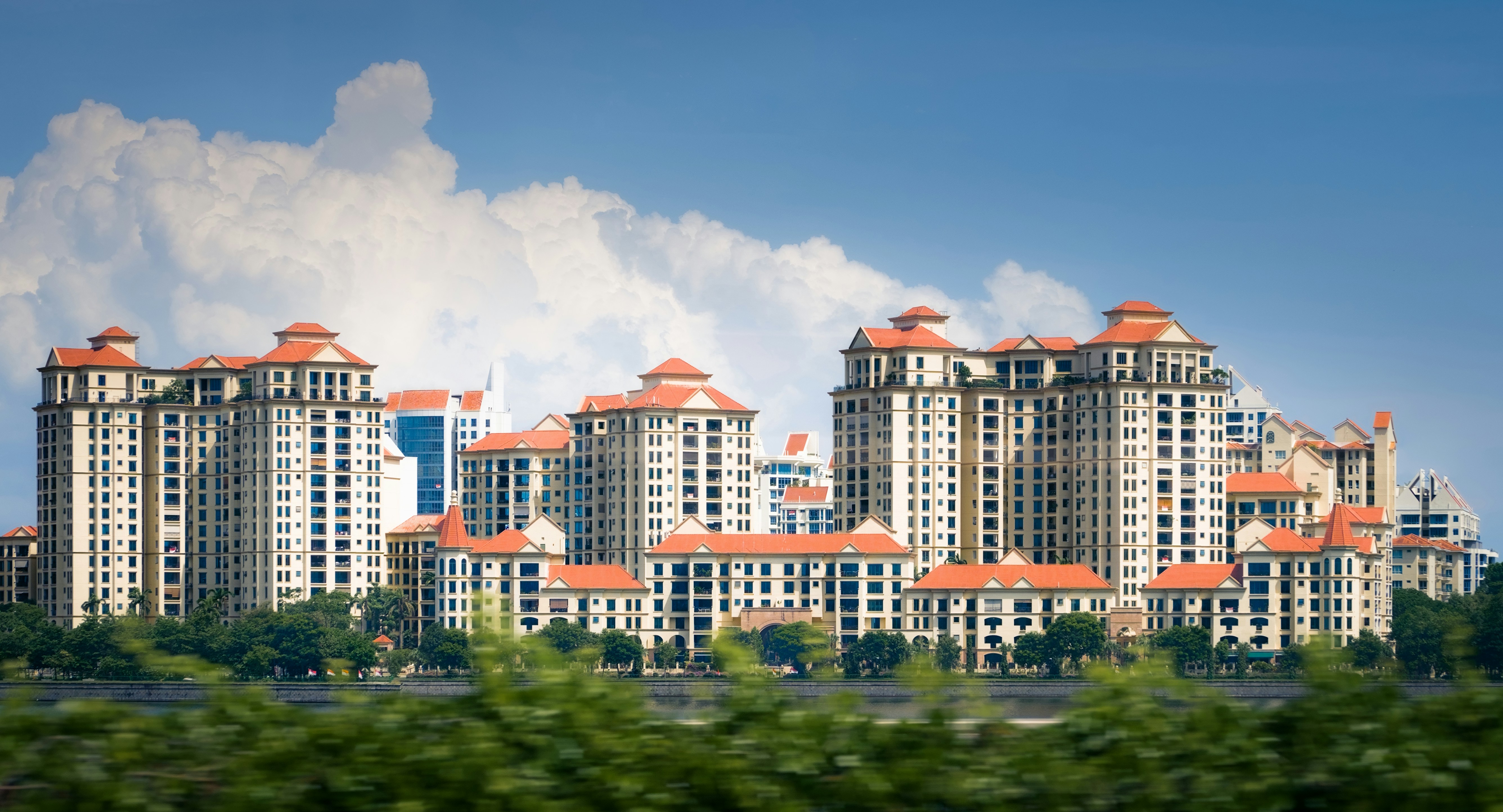 A row of modern residential buildings with distinct red-tiled roofs set against a bright blue sky, reflecting a blend of contemporary design and natural surroundings.