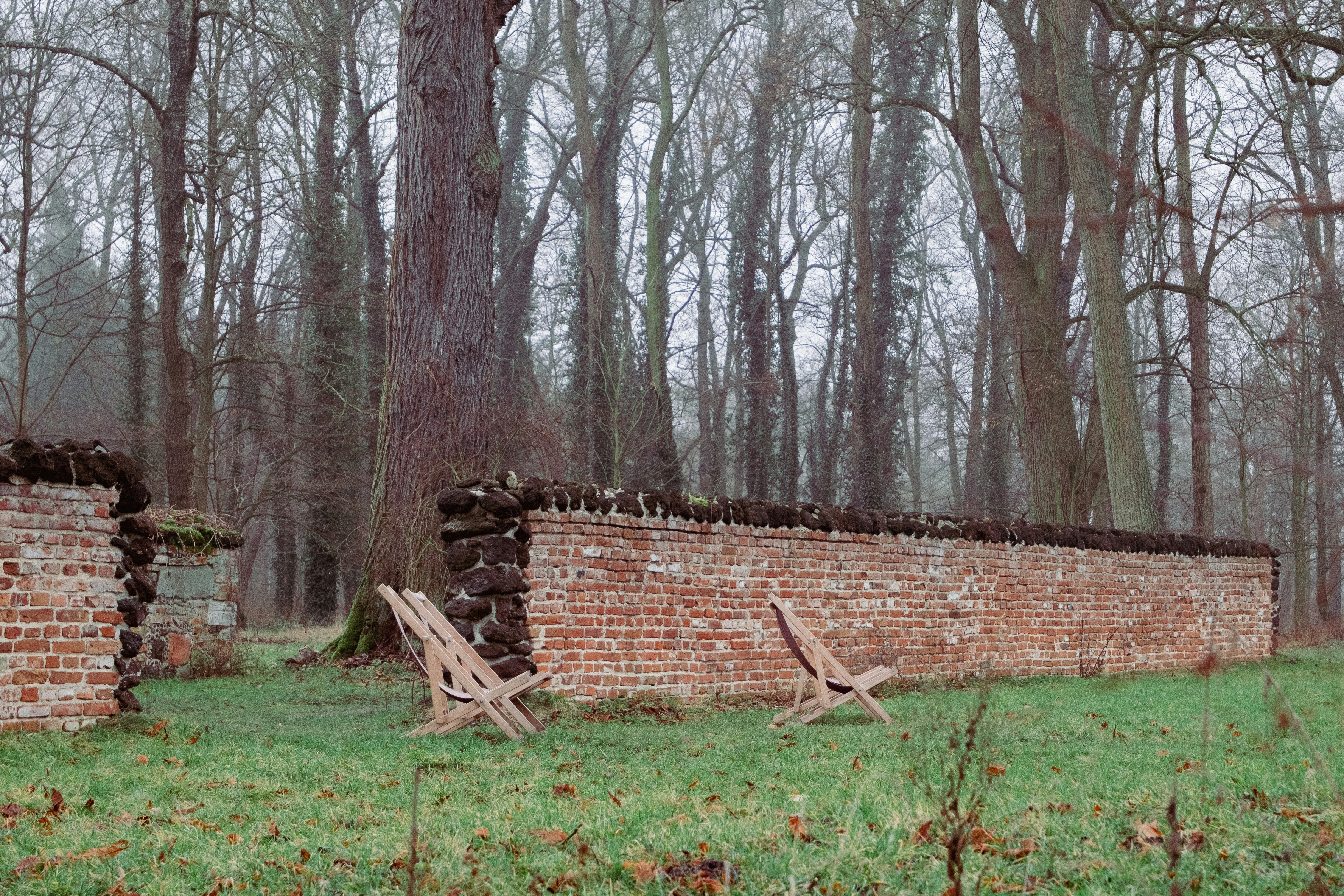 Weathered brick wall and toppled benches anchor a quiet park boundary