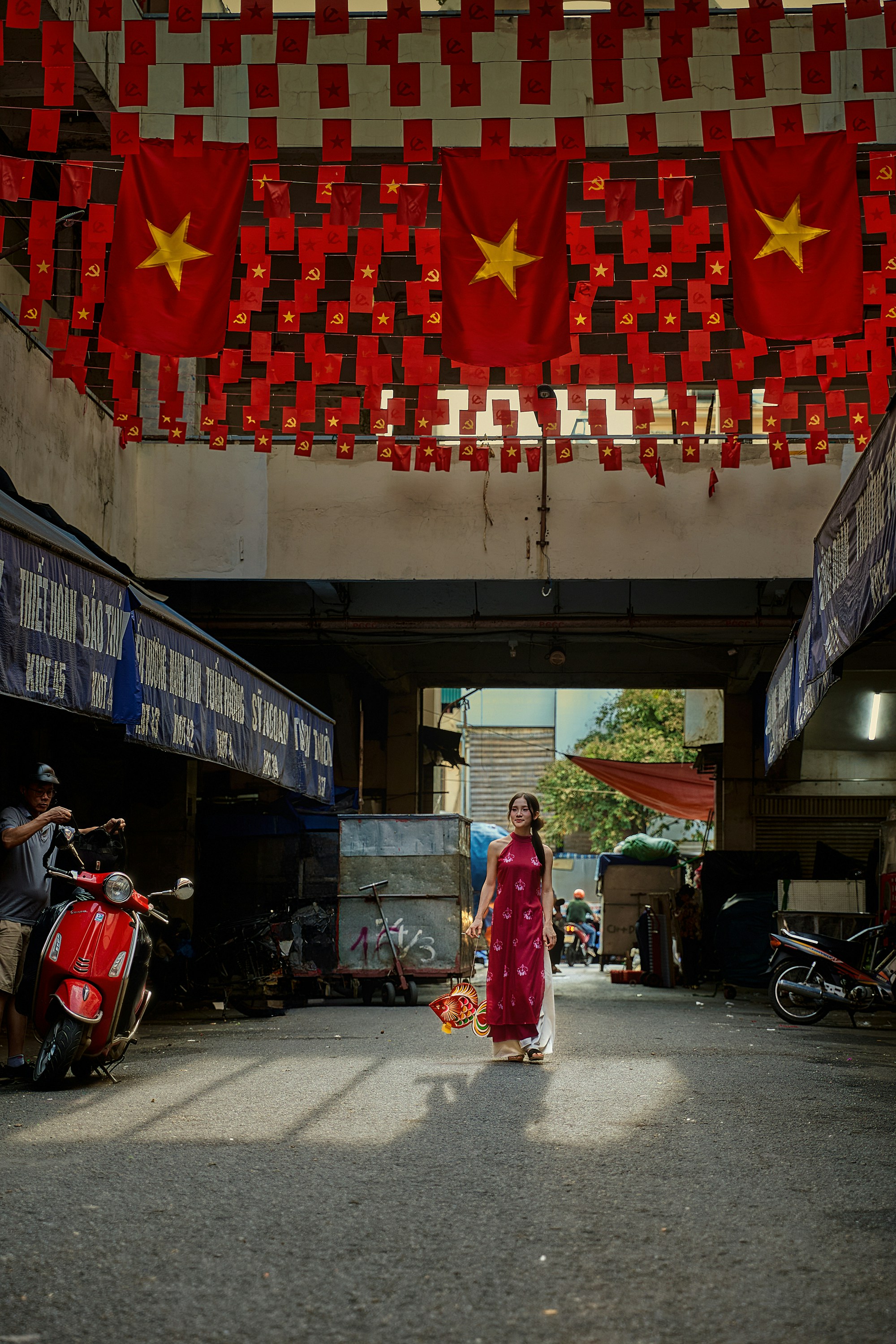 Woman in traditional attire walking through an alley adorned with vibrant flags, capturing the essence of cultural celebration in a bustling urban environment.