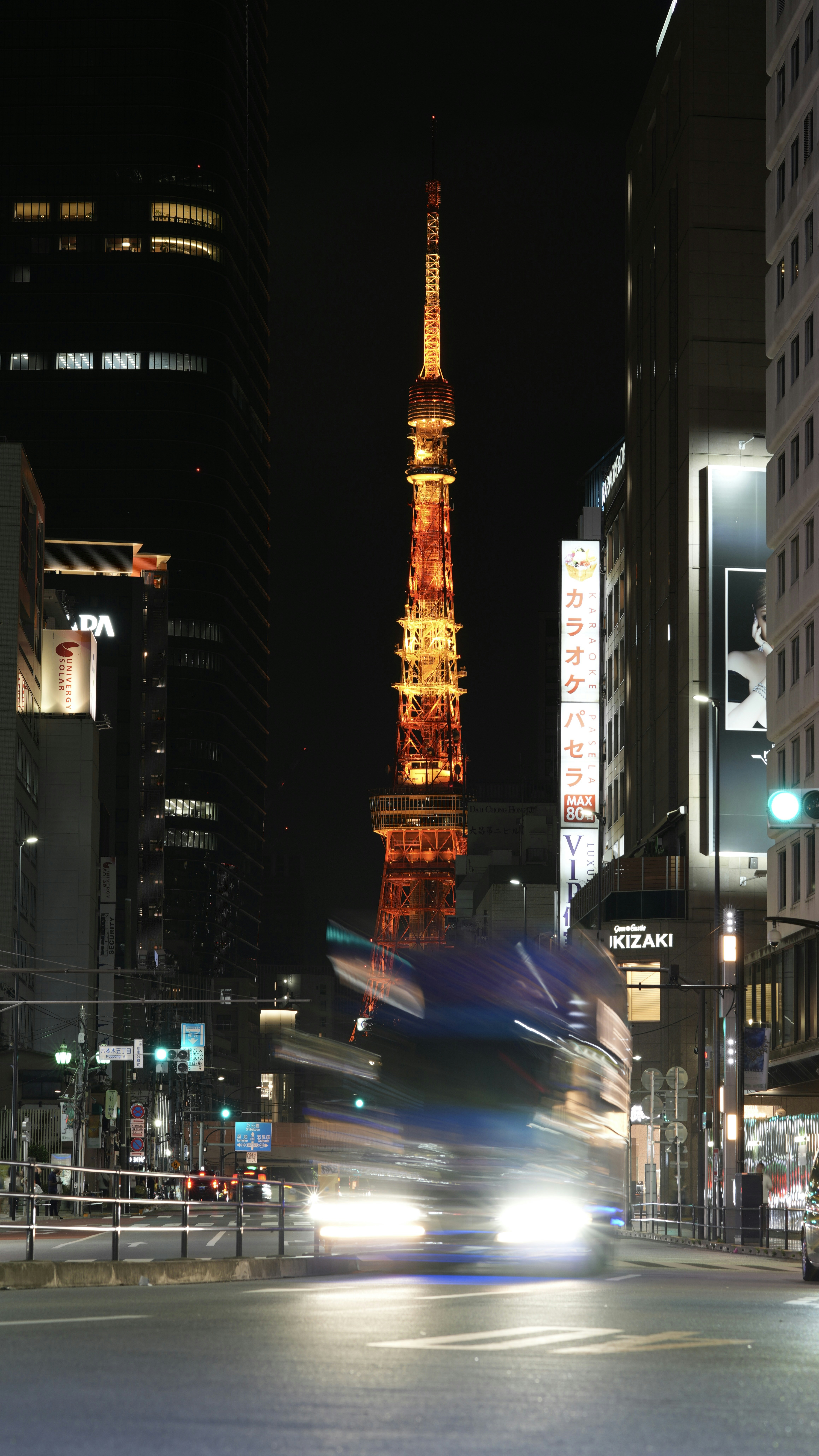 Tokyo Tower illuminated at night, surrounded by bustling city life and blurred motion of a passing bus.