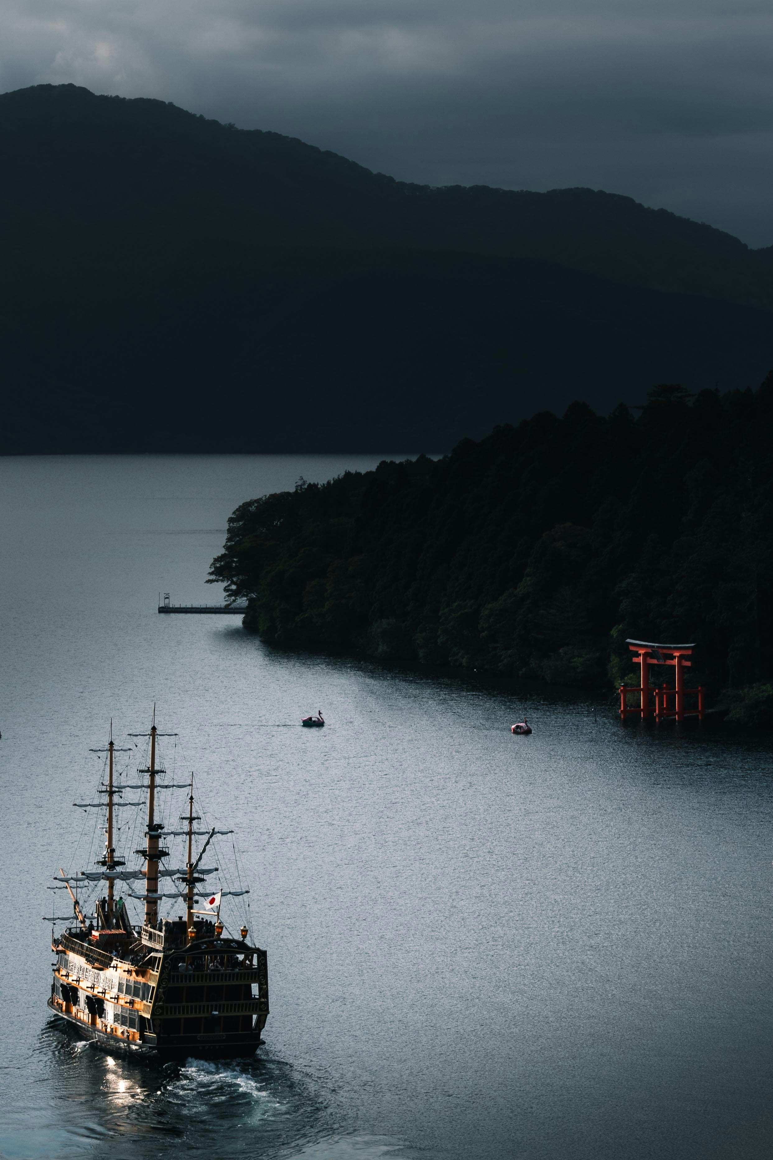 A large ship sails on a dark lake near mountains.