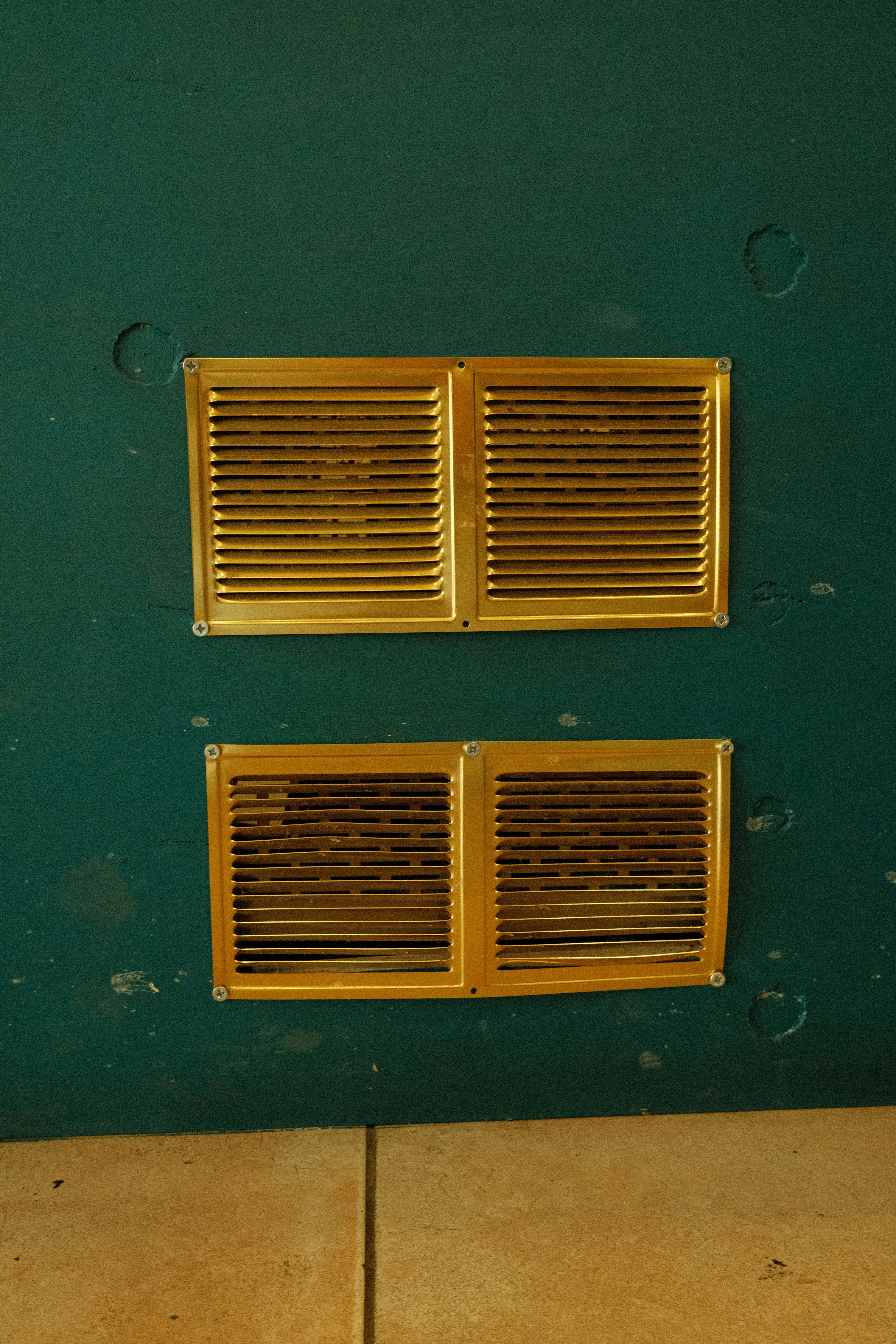 Two sets of golden air vent grilles mounted on a green wall, showcasing a blend of utility and aesthetics.