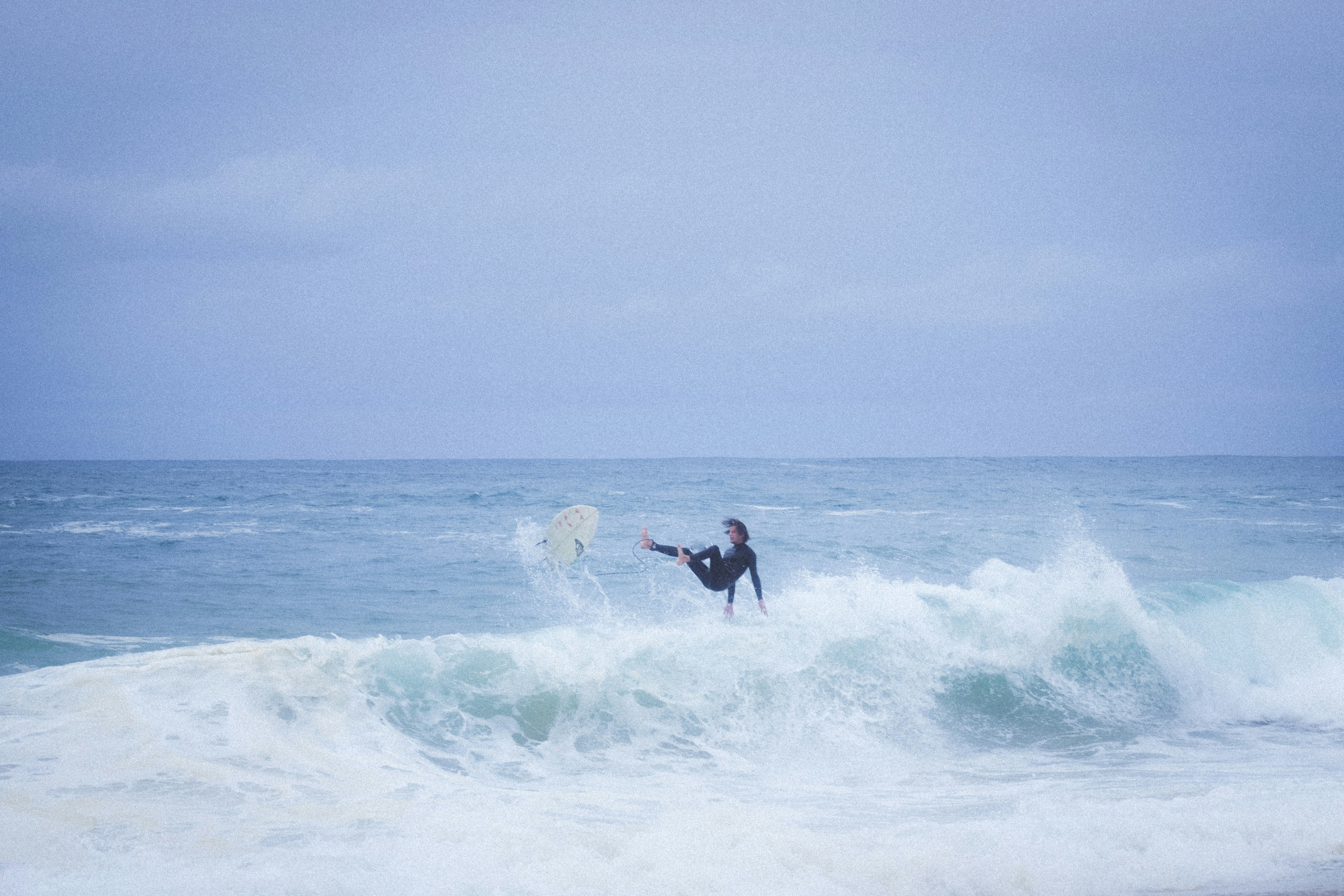 Surfer executing a dynamic maneuver atop a crashing wave under a cloudy sky.