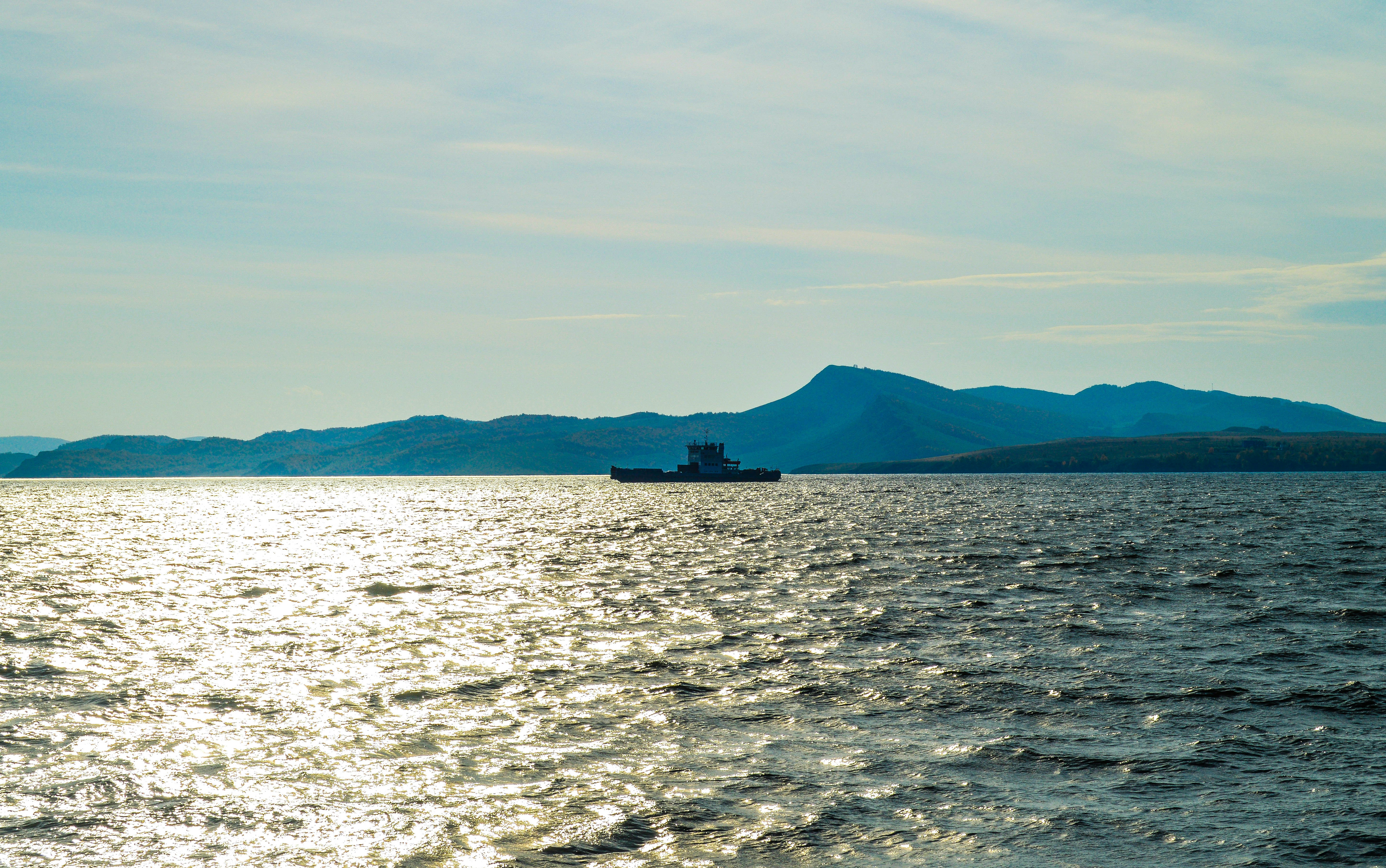 A solitary ship glides across shimmering waters, framed by distant mountains under a serene sky.