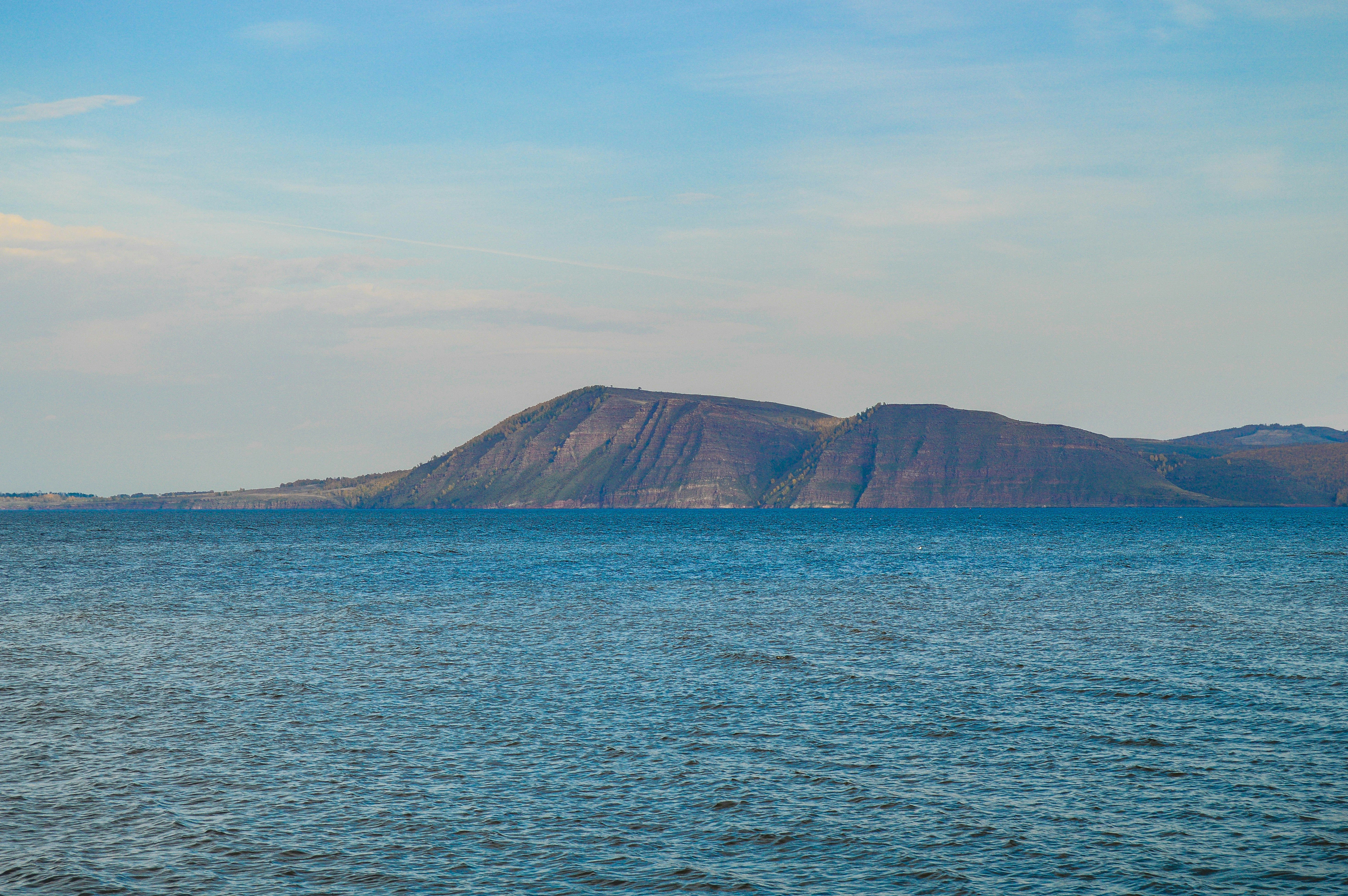 Distant hills rise majestically above a calm sea, reflecting the soft hues of the sky. The scene captures the serene beauty of a coastal landscape.