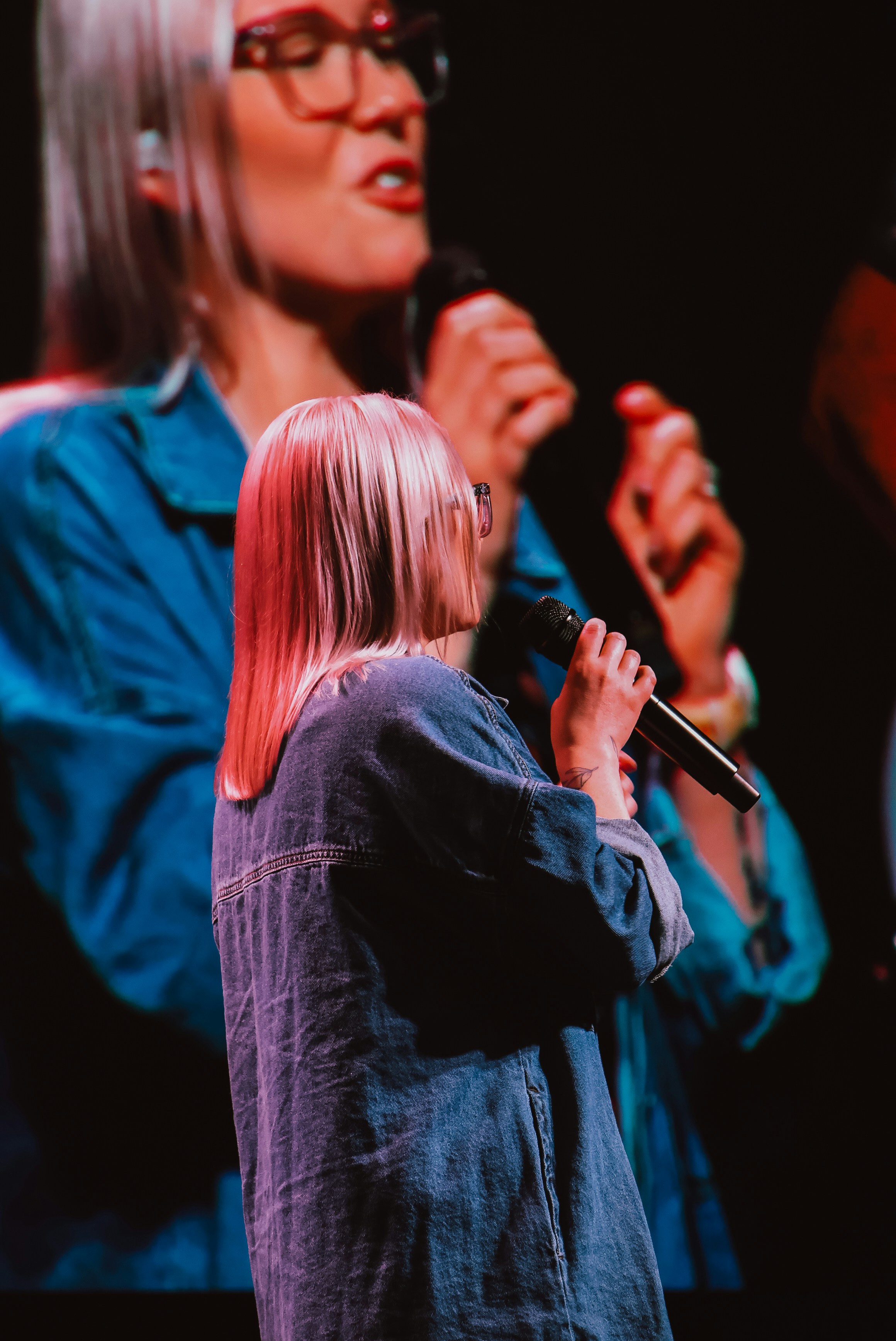Two women singing into microphones on stage.