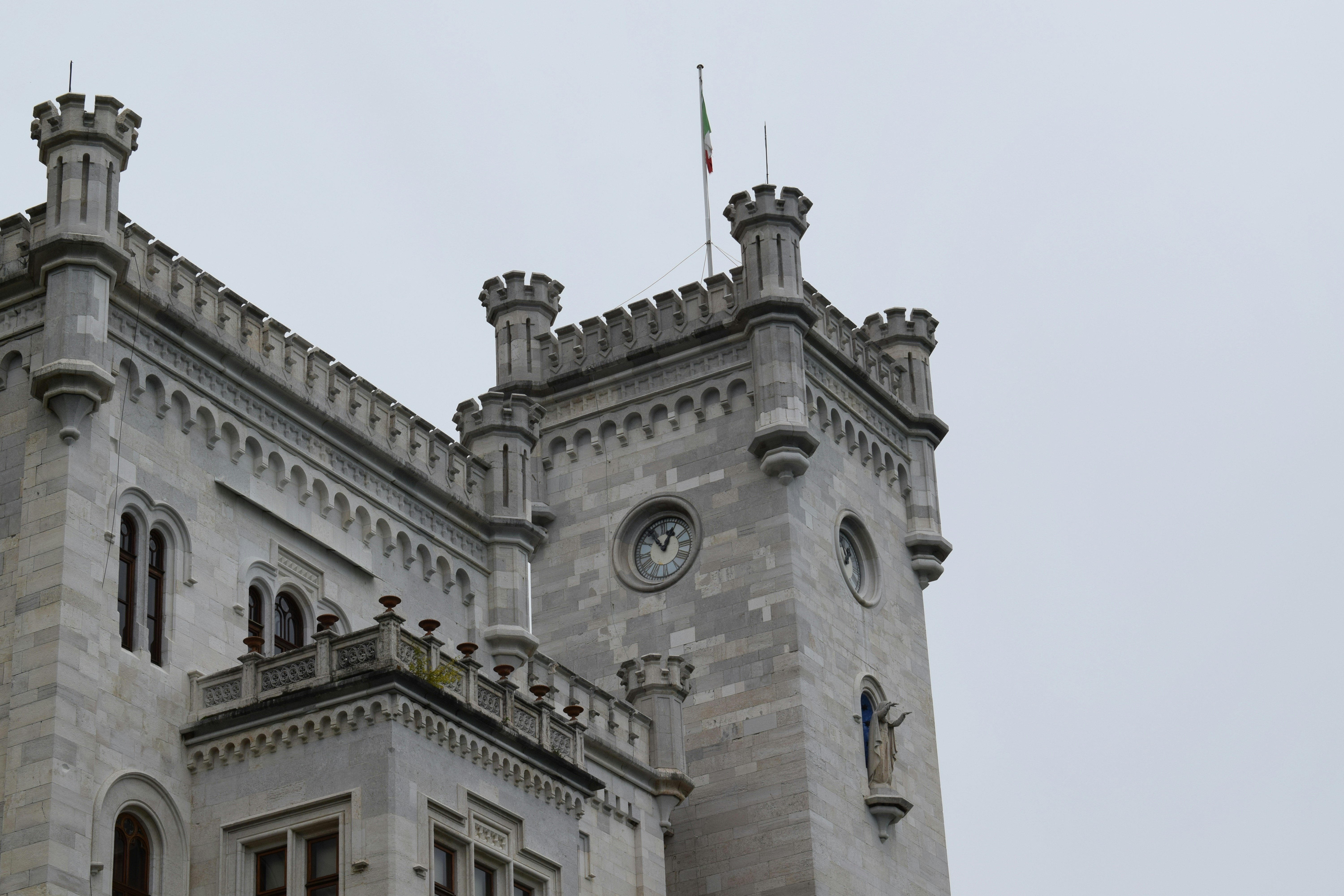 Historic castle tower adorned with intricate stonework and a flag atop, showcasing its majestic presence against a gray sky.