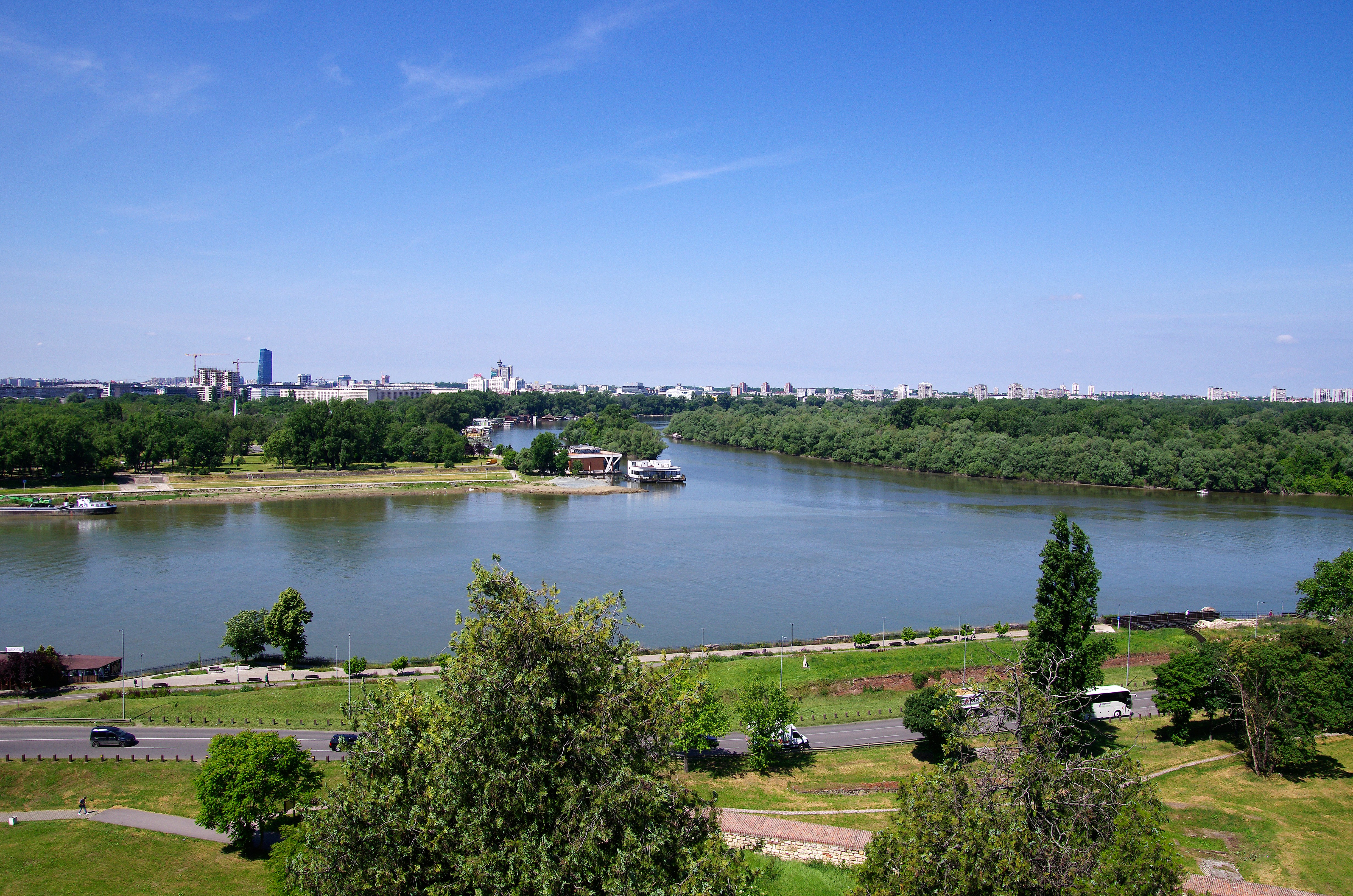 Lush riverside landscape with a winding river reflecting the sky and urban skyline in the distance. The scene captures the harmony between nature and city life.