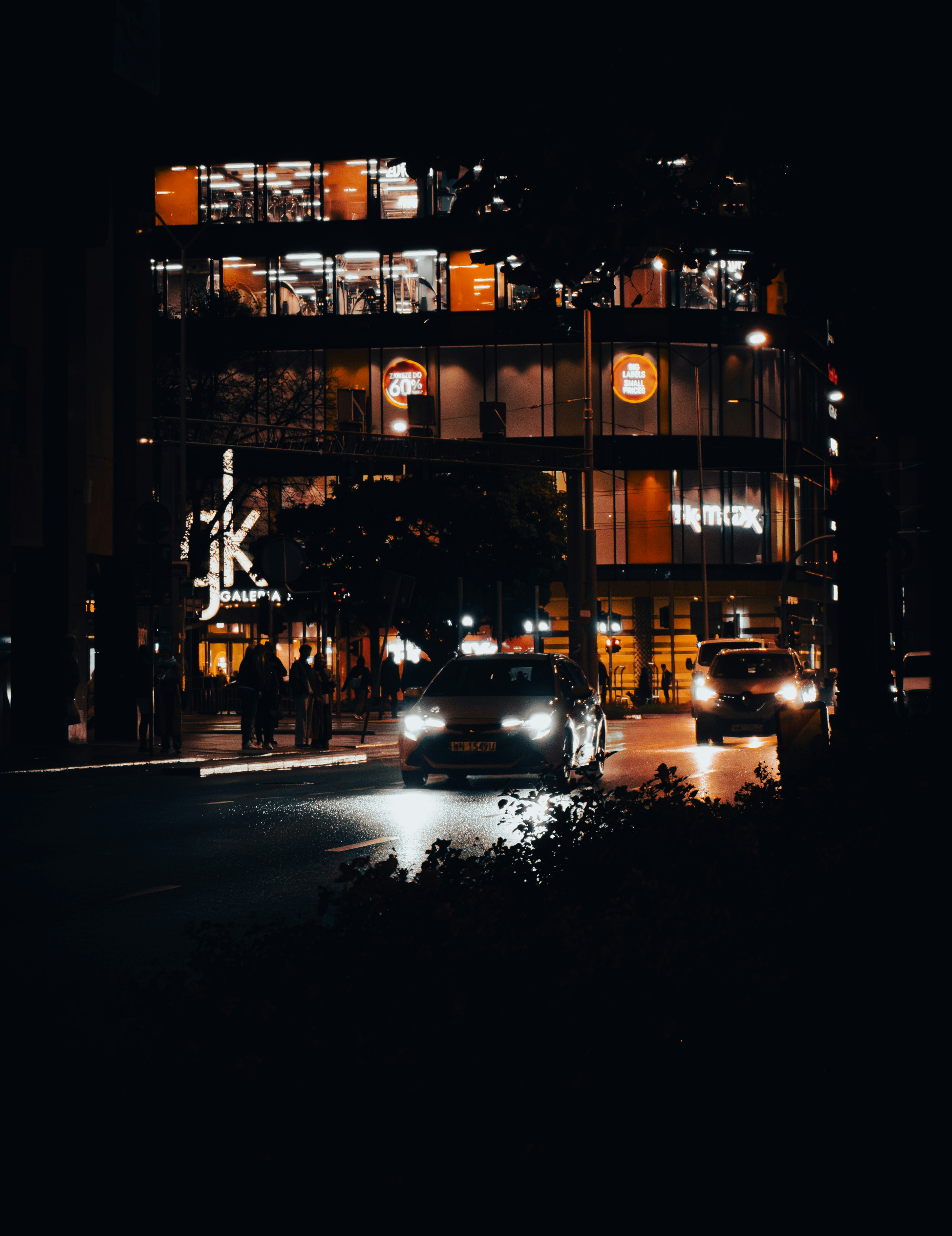 Cars driving past a brightly lit building at night
