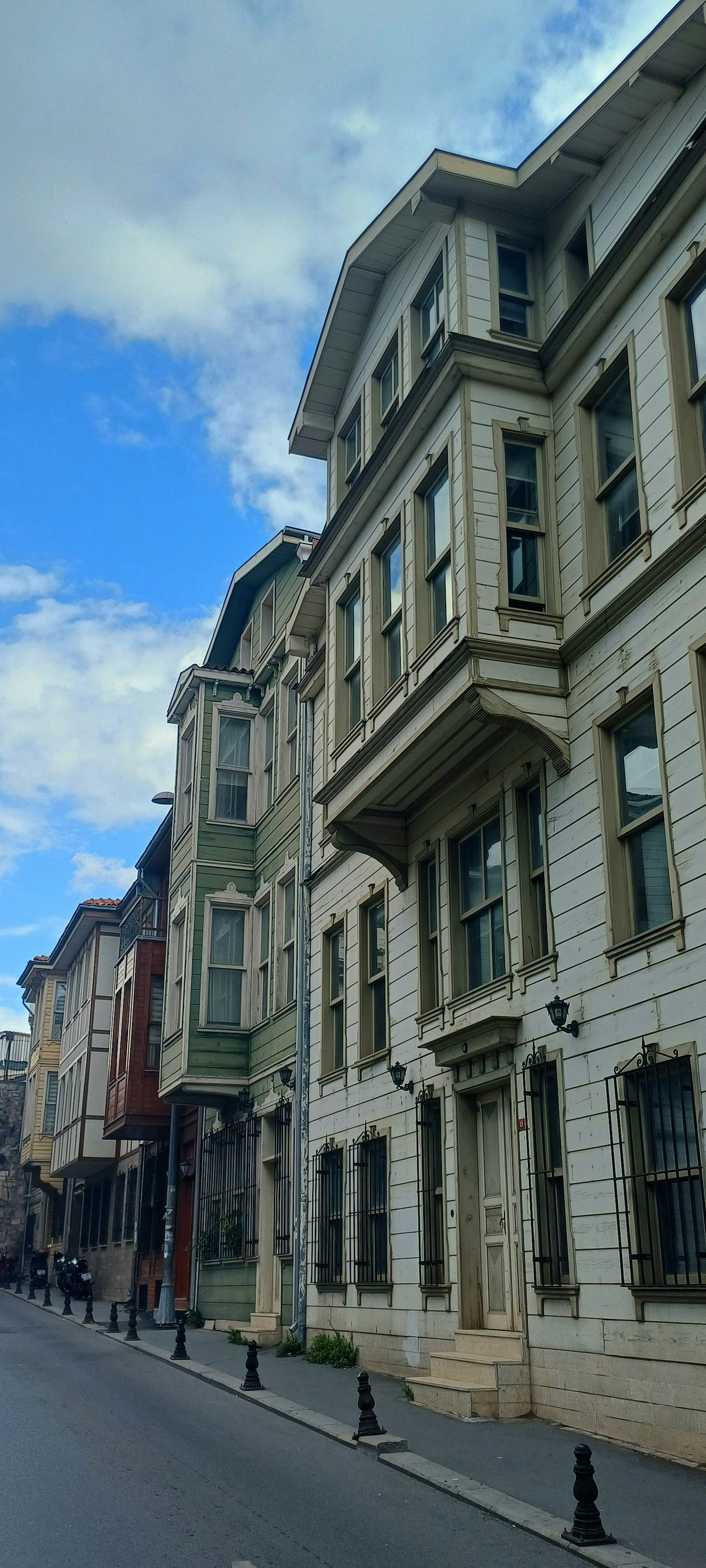 Colorful historical buildings line a narrow street under a cloudy sky, showcasing intricate architectural details. The scene captures the essence of urban heritage.