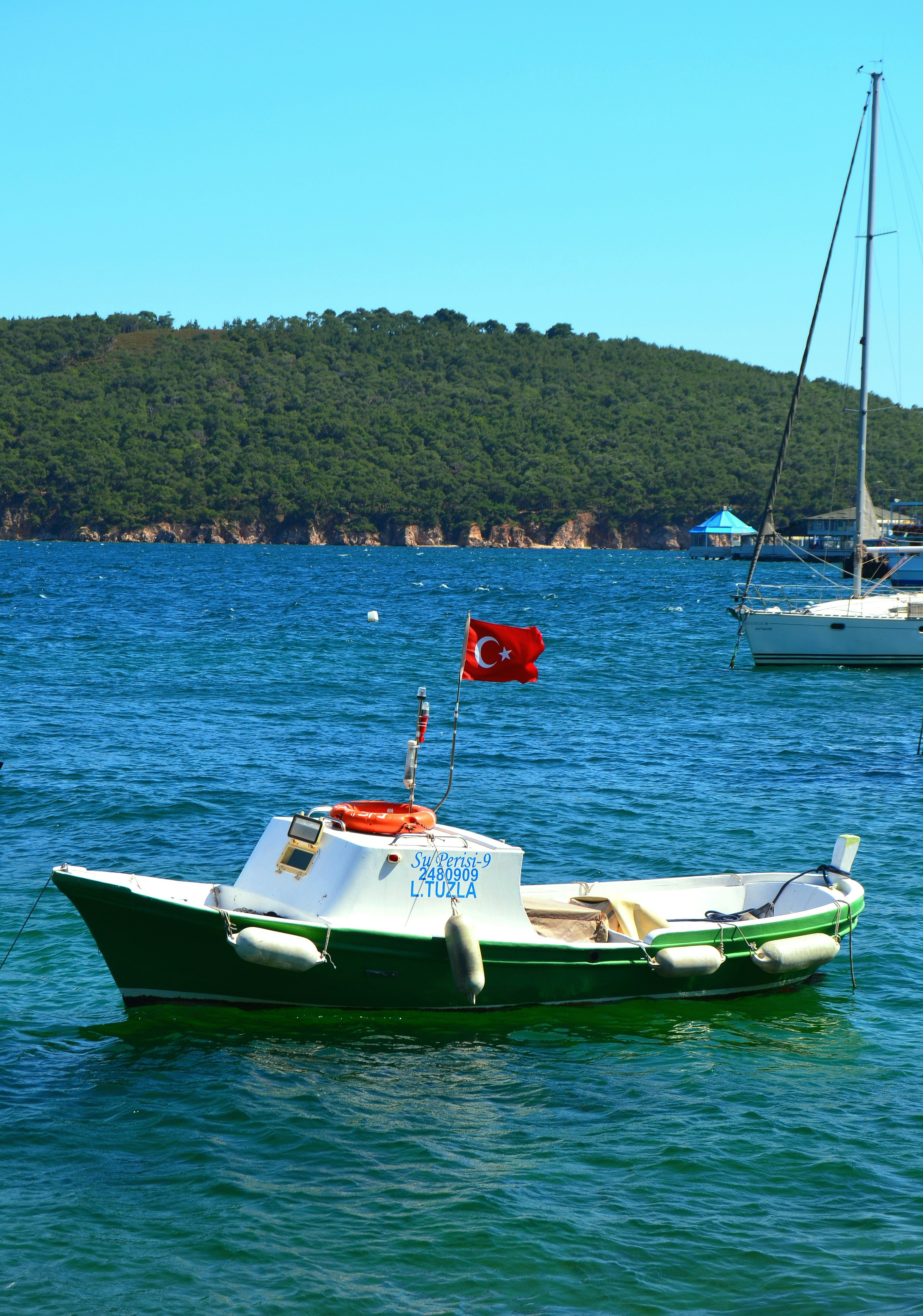 A traditional fishing boat with a Turkish flag floats in vibrant turquoise waters, framed by lush green hills in the background.