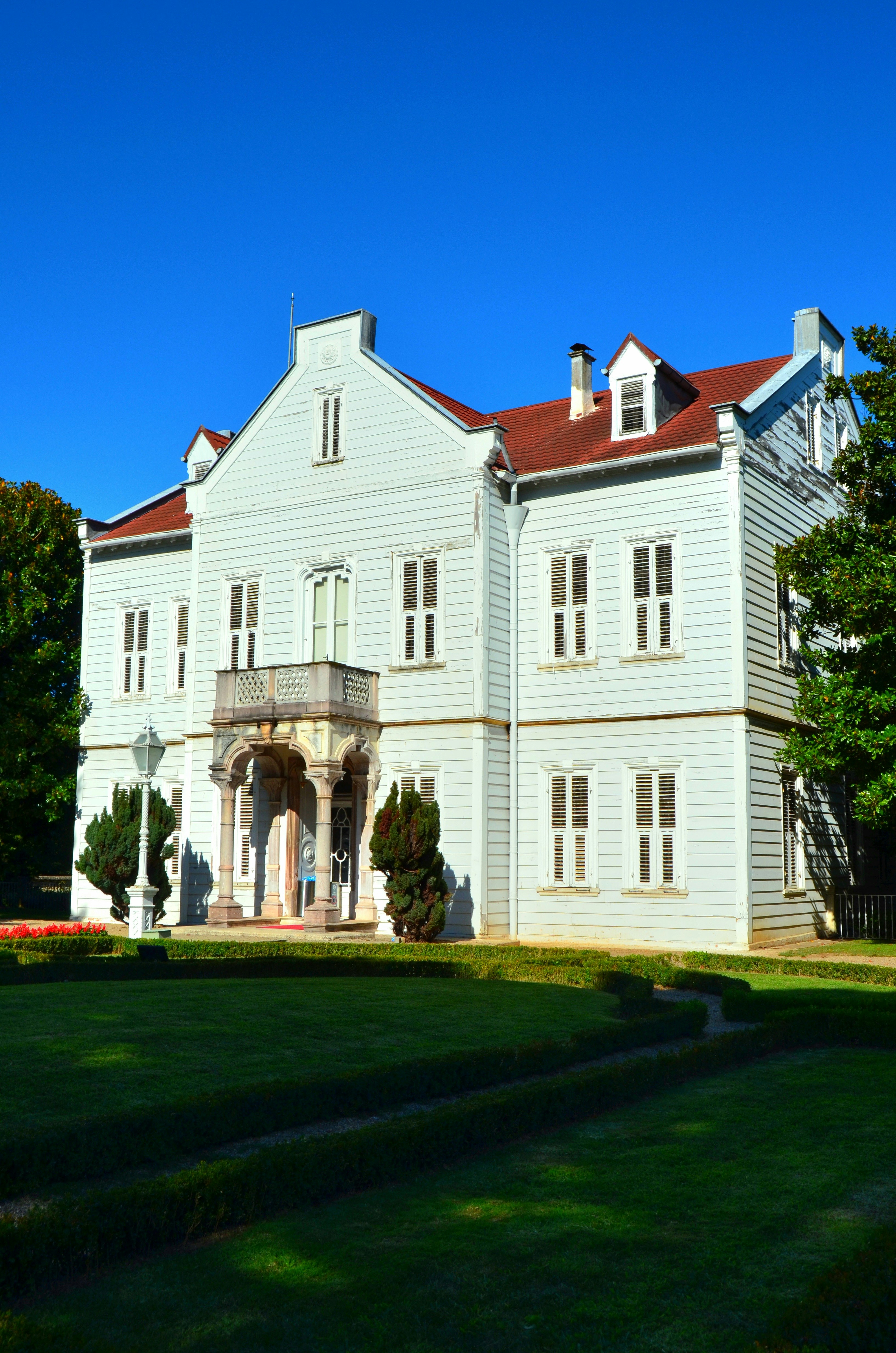 Sunlit Manor: Pale-Blue Facade, Crimson Roof, and Formal Terraces