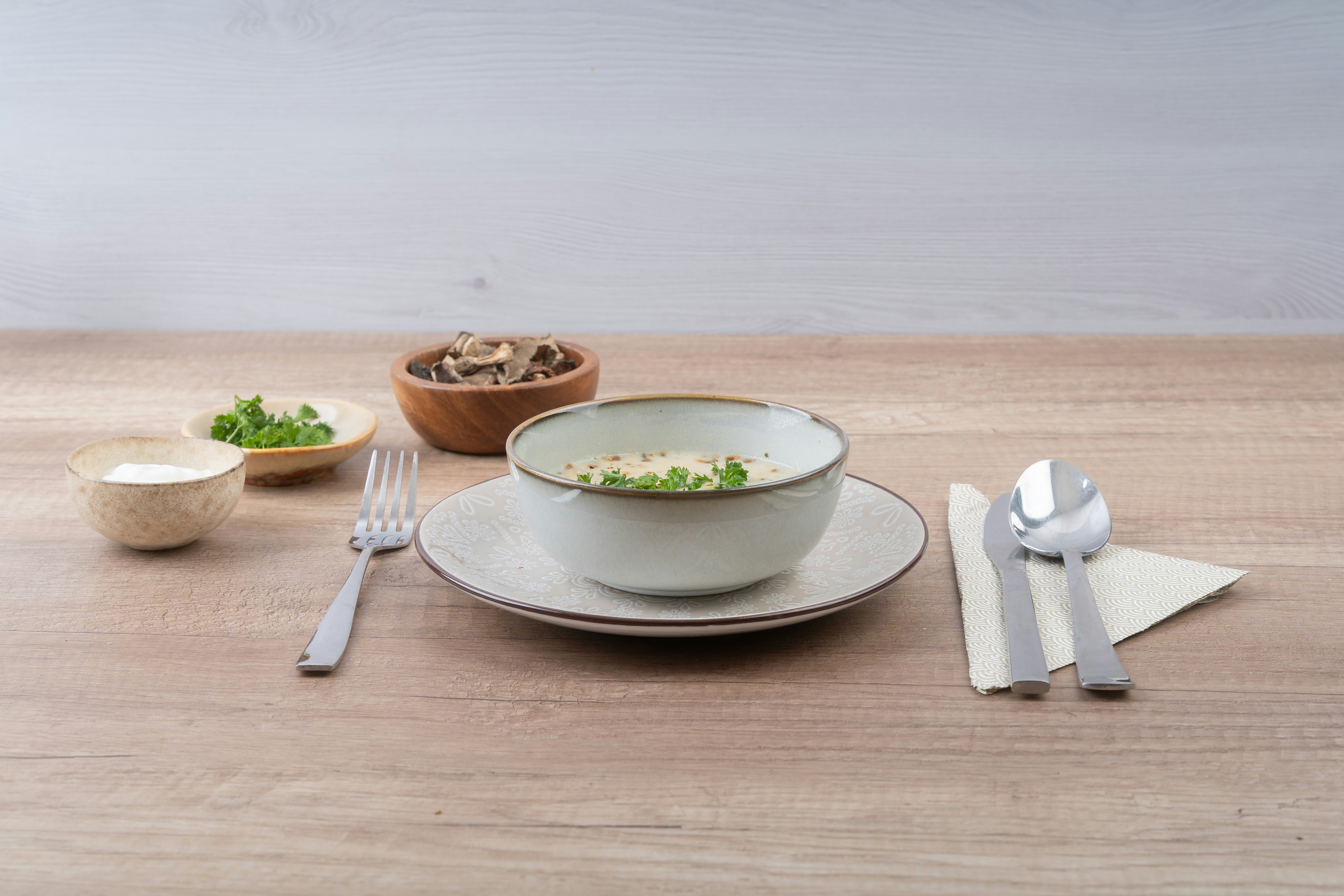 Photo of a fully set table. | Bowl of soup with ingredients and cutlery on table