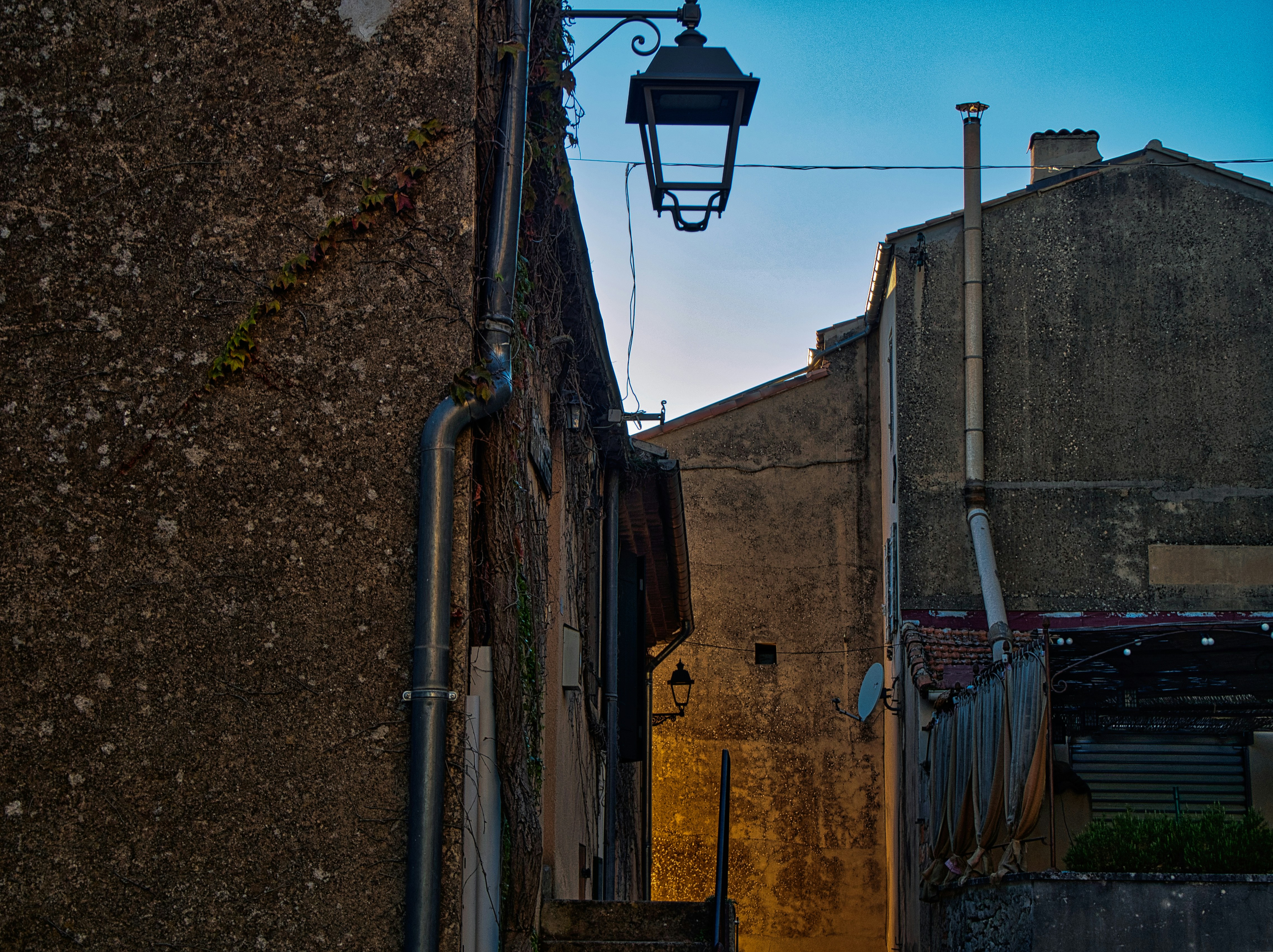 Old street lamp illuminates narrow alleyway at dusk.