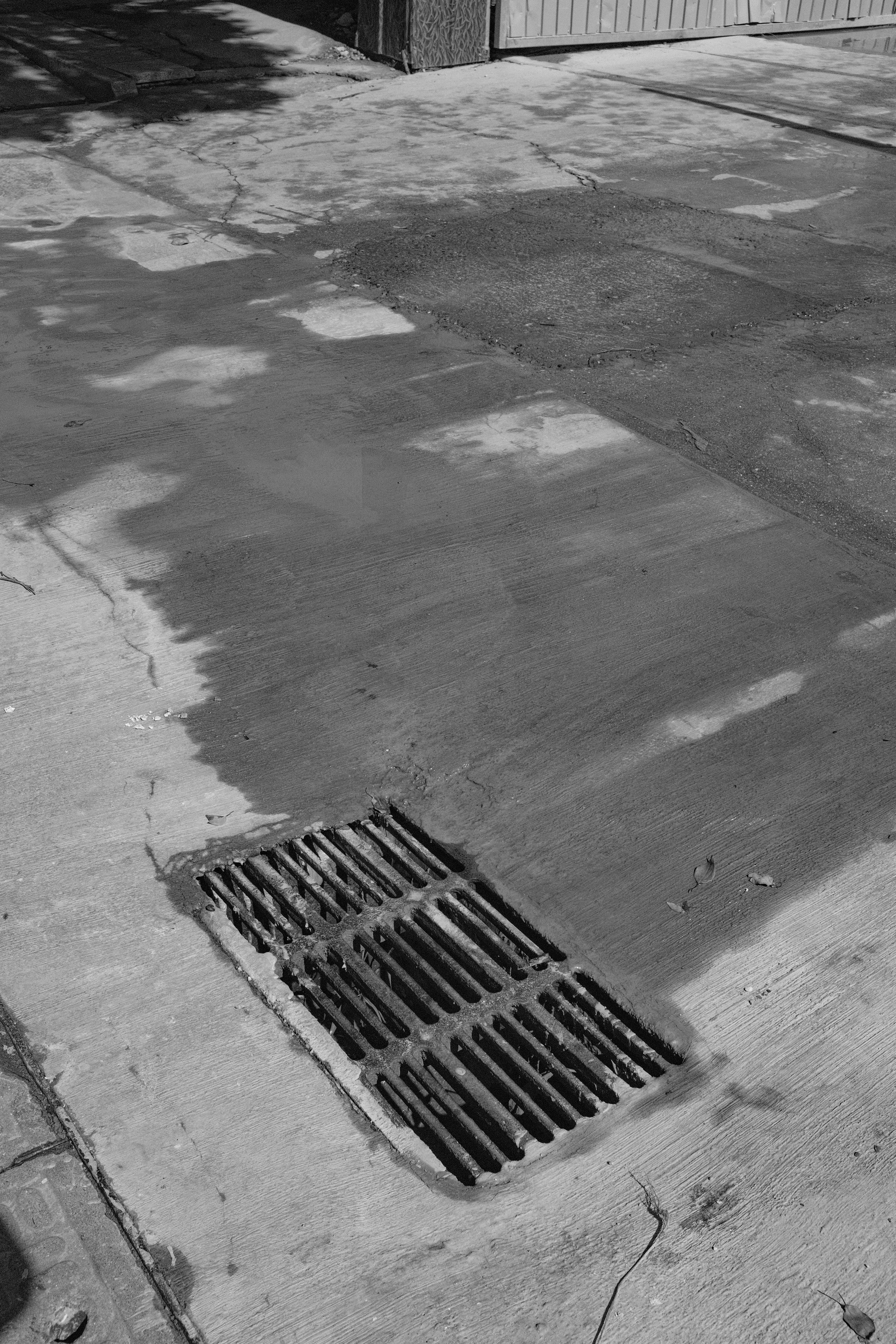 Grate embedded in a weathered concrete surface, showcasing the interplay of light and shadow in an urban setting.