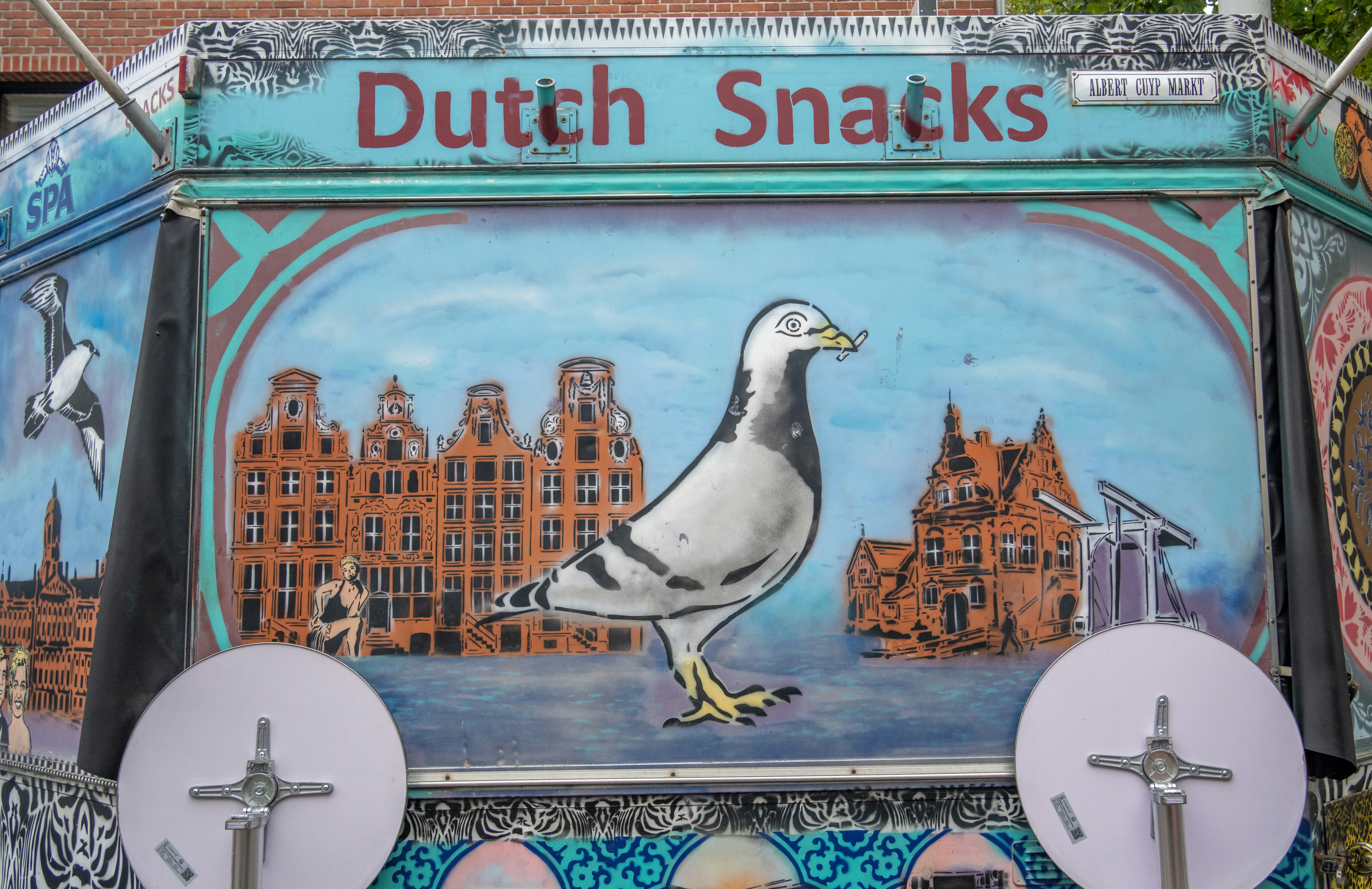 Vibrant mural featuring a pigeon and traditional Dutch architecture, advertising a snack stall. The artwork combines cultural elements with a playful twist.