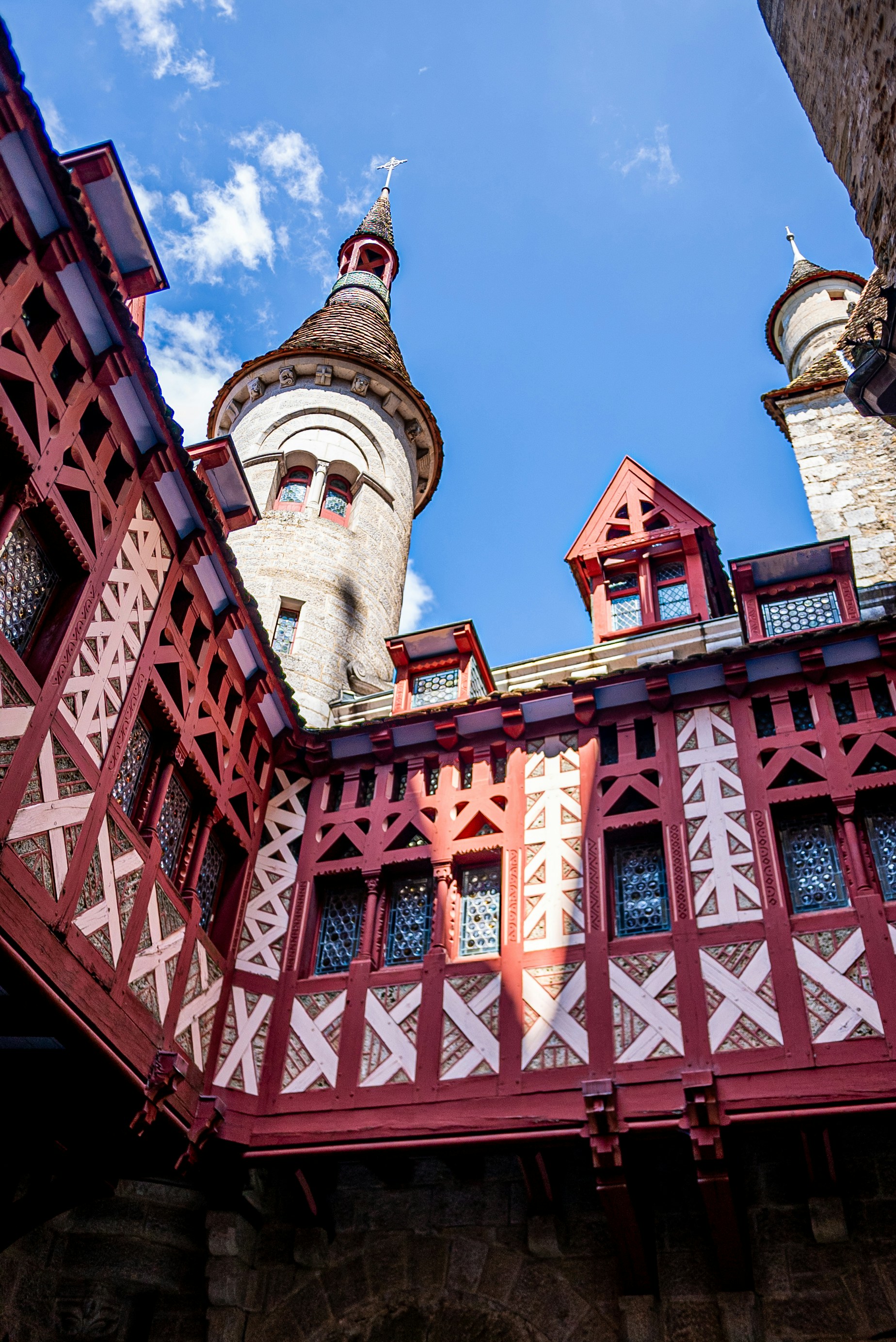 Intricate red and white timber framing of a historic castle courtyard under a bright blue sky.