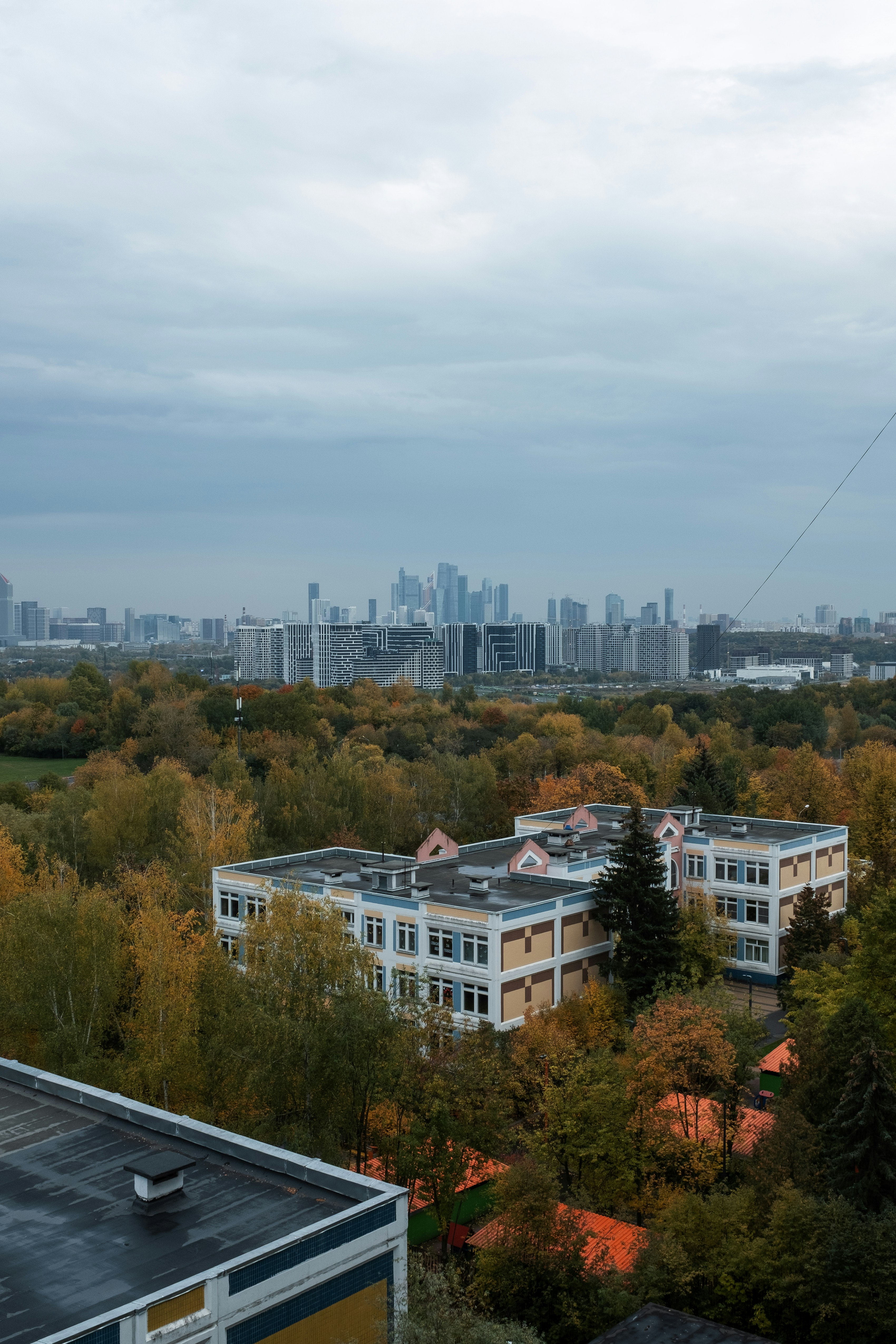 View of a city skyline framed by vibrant autumn foliage and a school building, showcasing the contrast between urban life and nature's beauty.