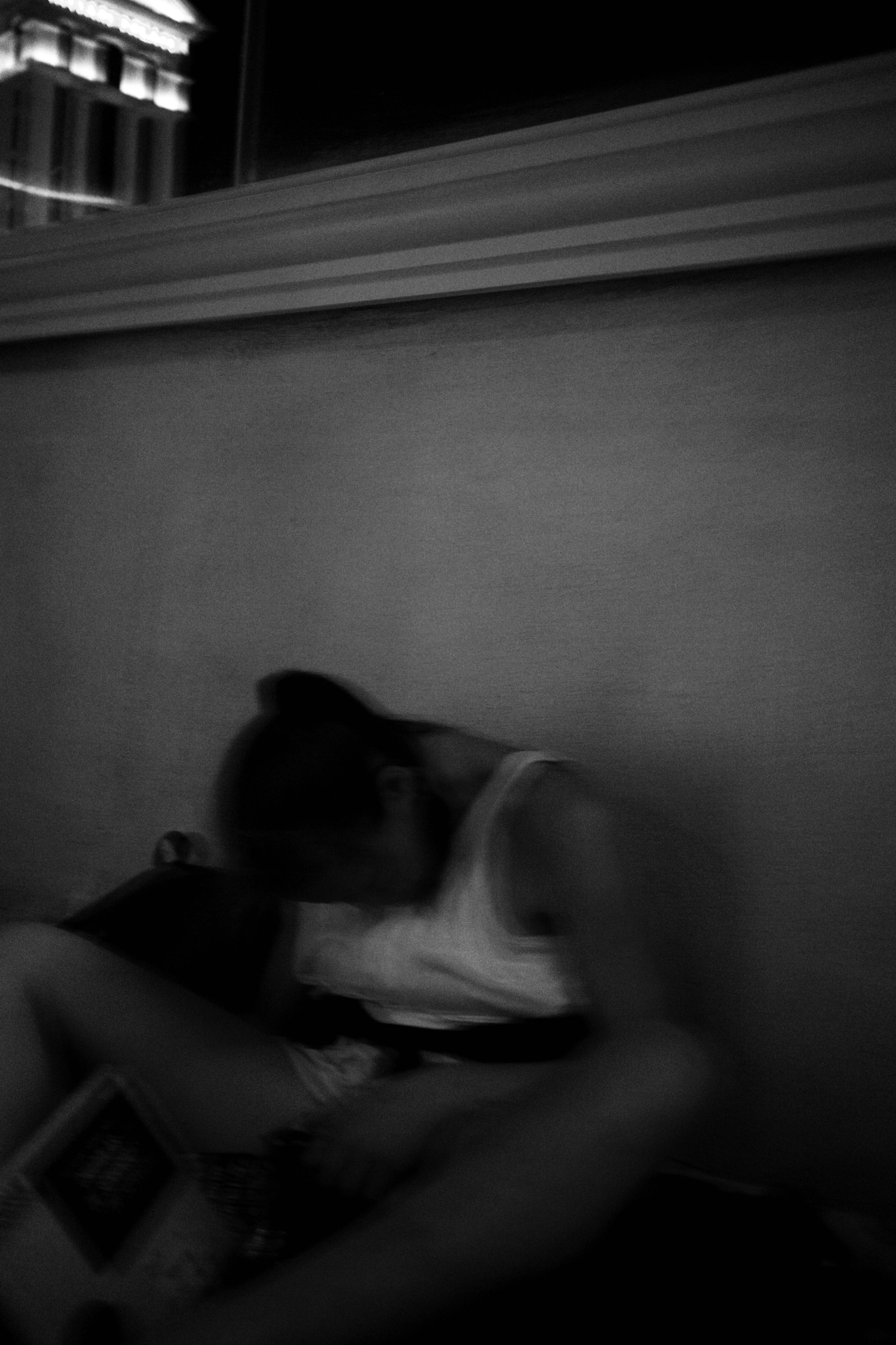 A person in a white tank top sits in a dimly lit space, absorbed in a book, creating a sense of introspection and quietude.
