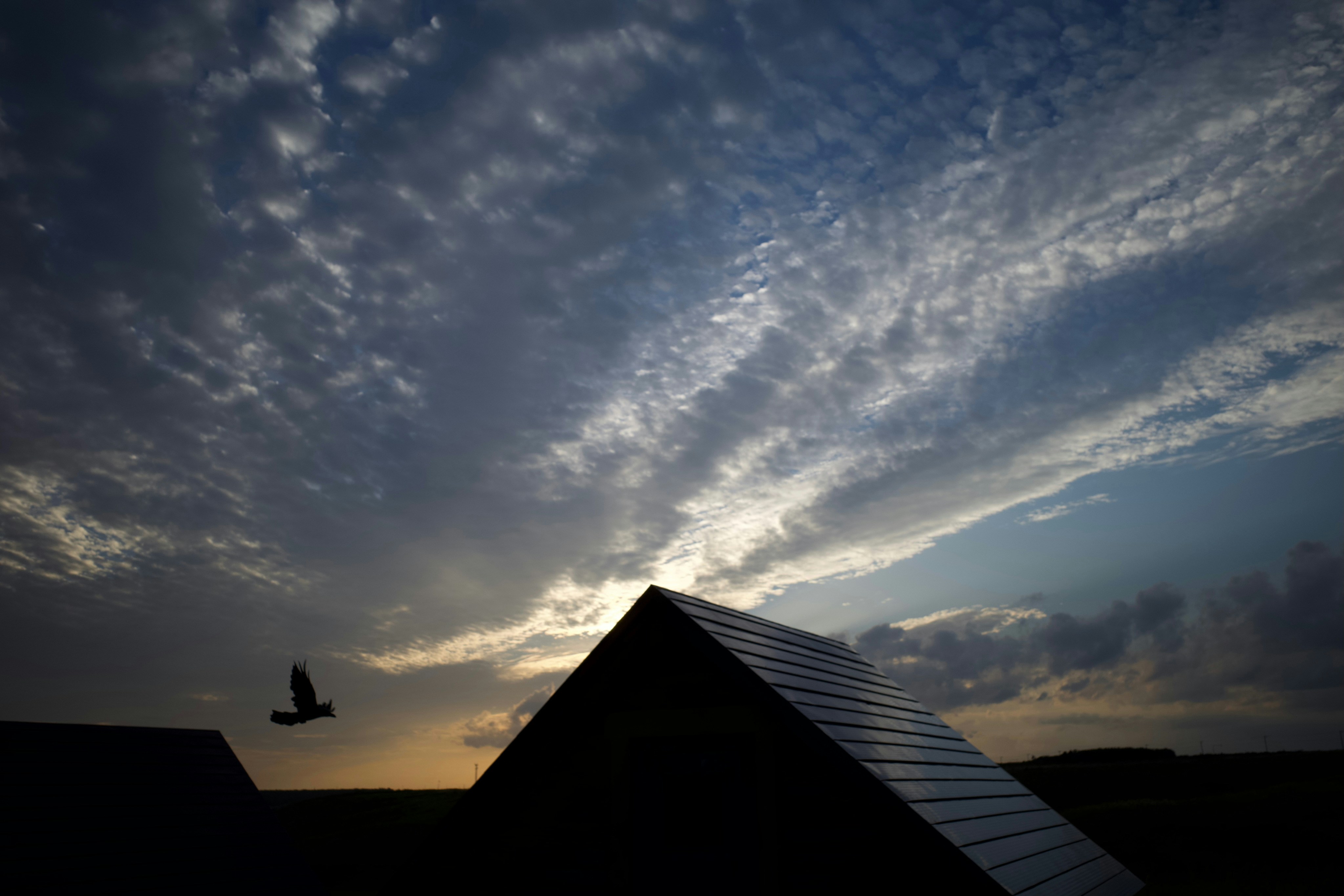 Silhouette of pyramid against dramatic cloudy sky at sunset.
