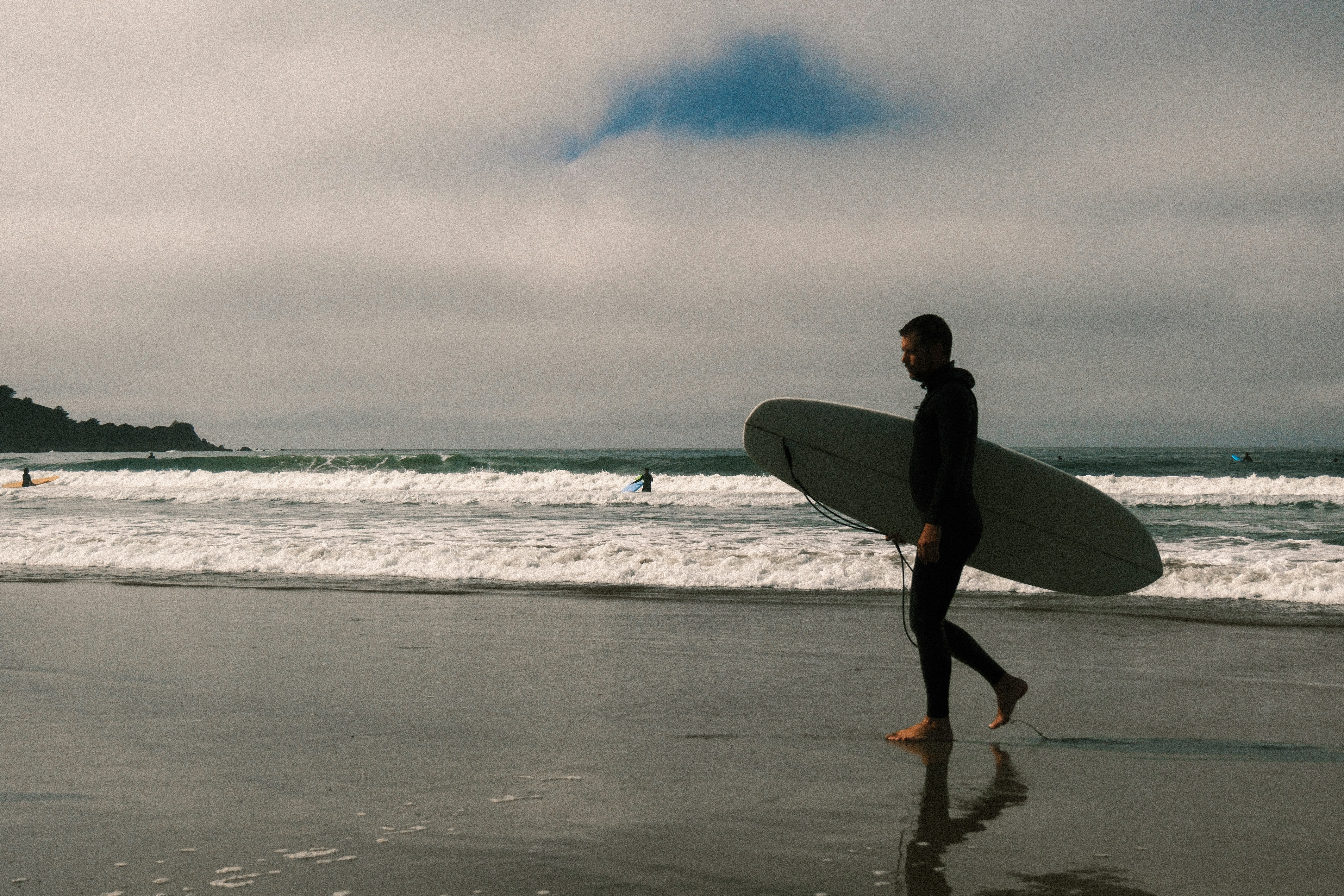 Surf Rider at the Edge: A Surfer Steps Ashore with a Longboard Against a Greying Sea