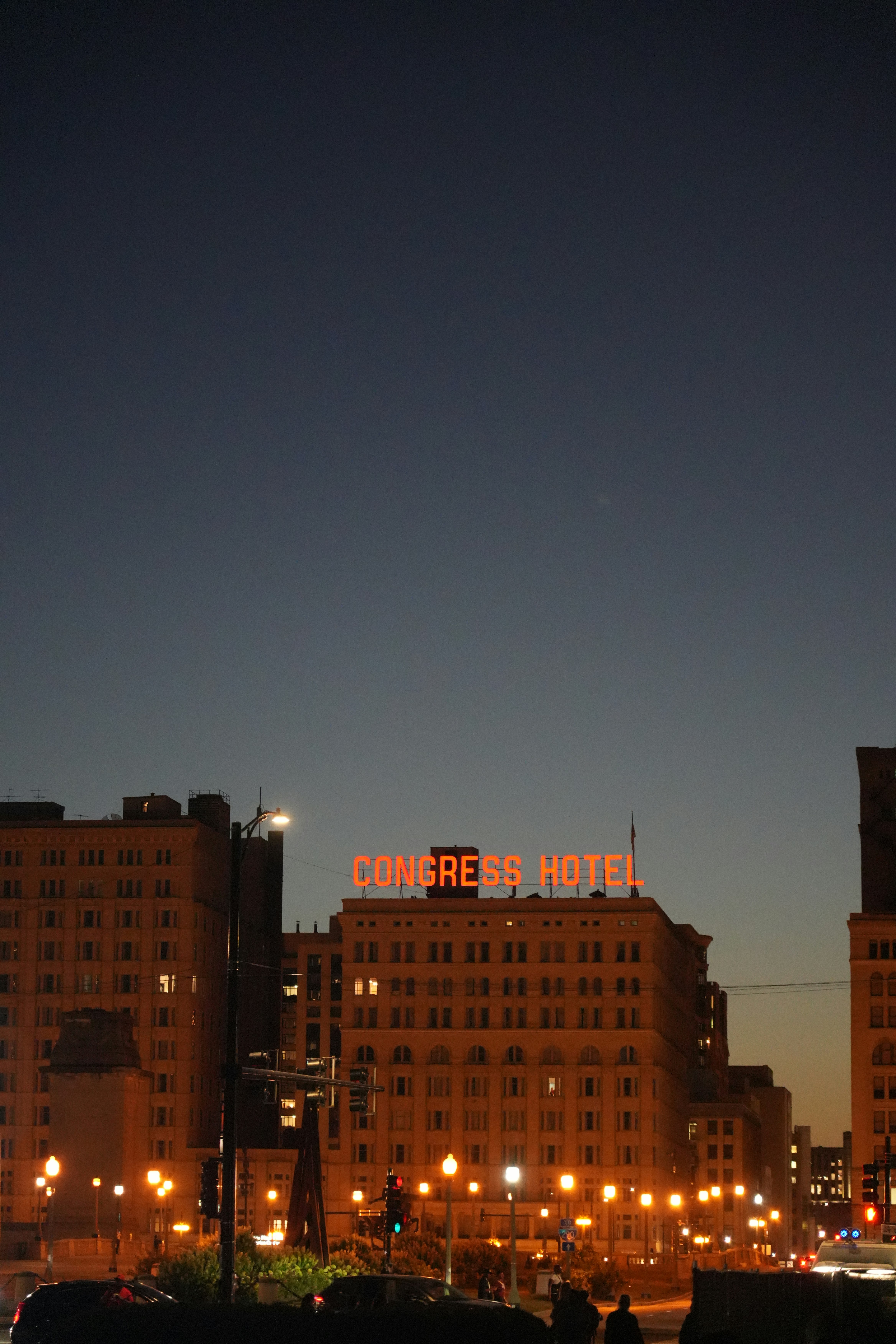 The Congress Hotel stands illuminated against a twilight sky, showcasing its vintage neon signage amidst the urban landscape.