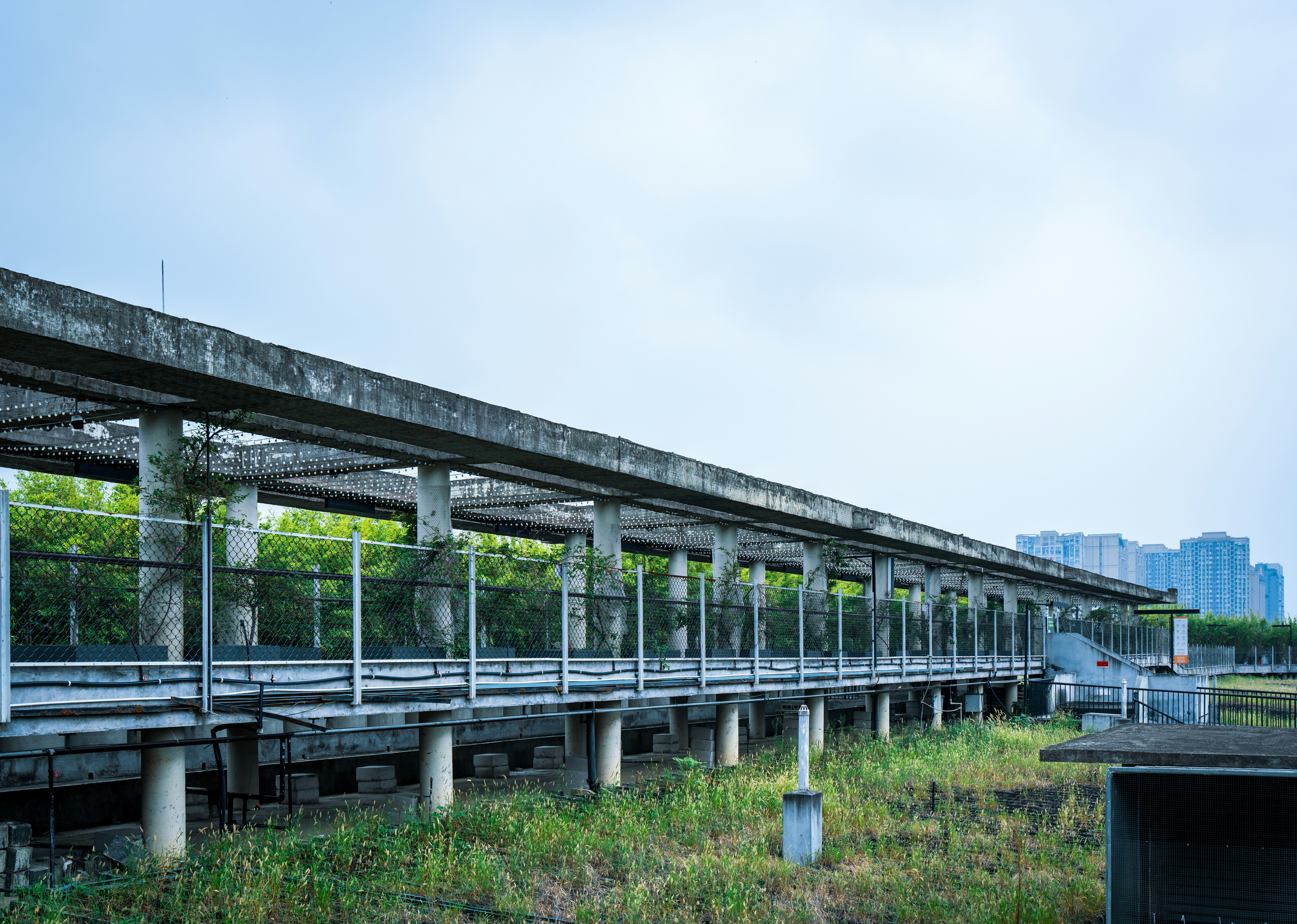 West Village Basis Yard | Overgrown structure with concrete pillars and fence.