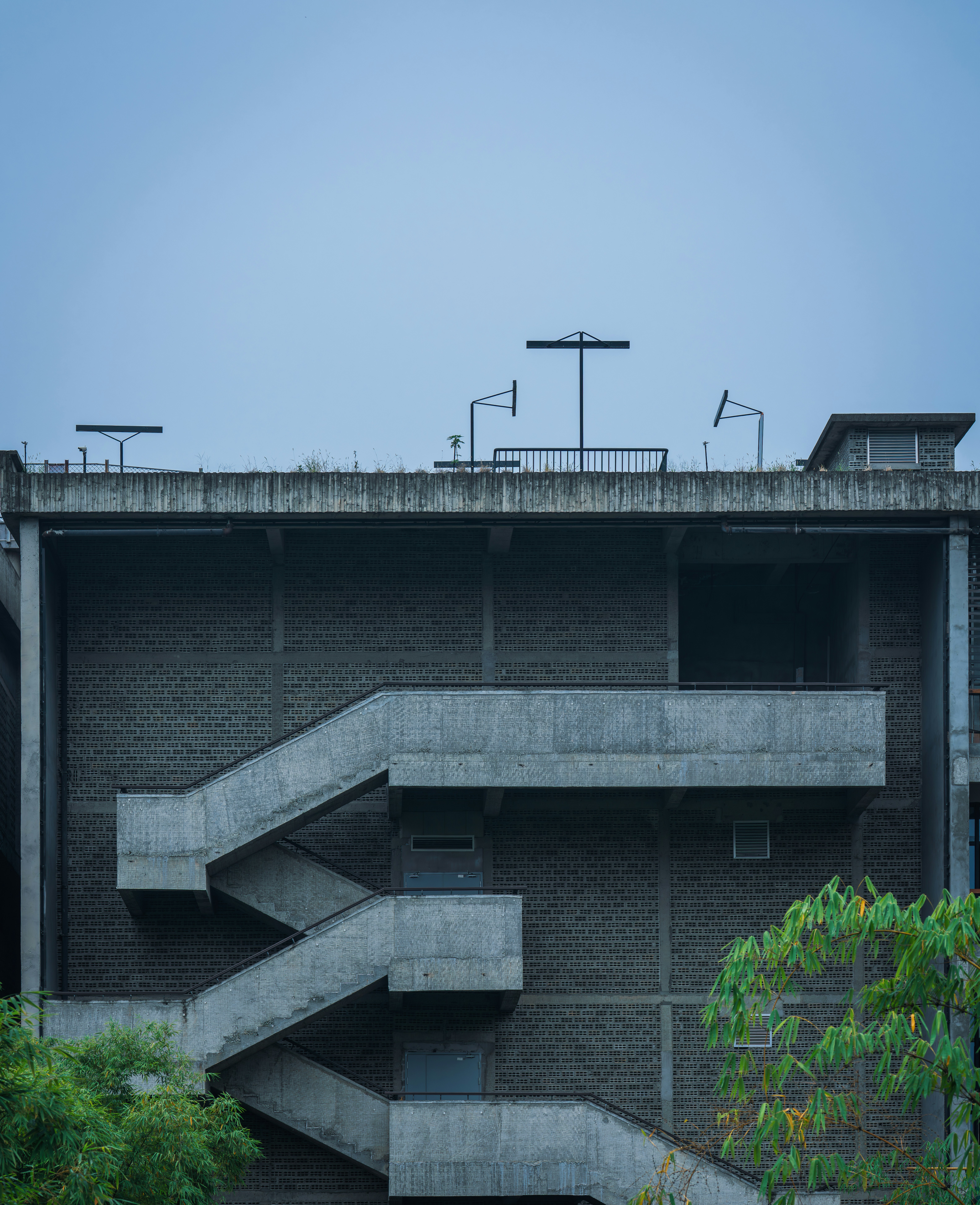 A stark concrete building facade featuring an angular staircase, framed by a muted sky. The scene highlights urban architecture's raw simplicity.