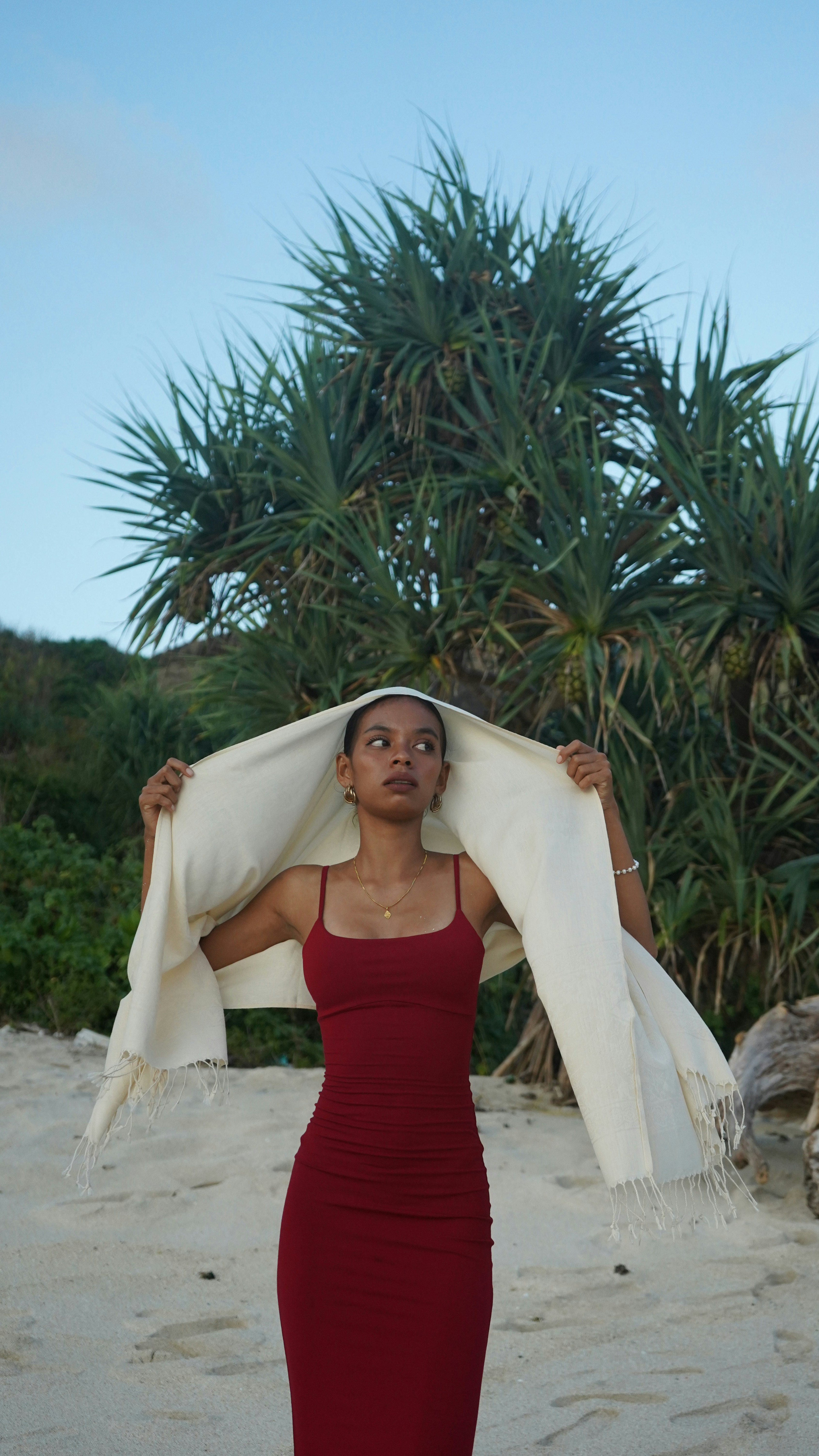 Beautiful girl in red dress on white sand beach. | Woman in red dress holding white shawl on sandy beach