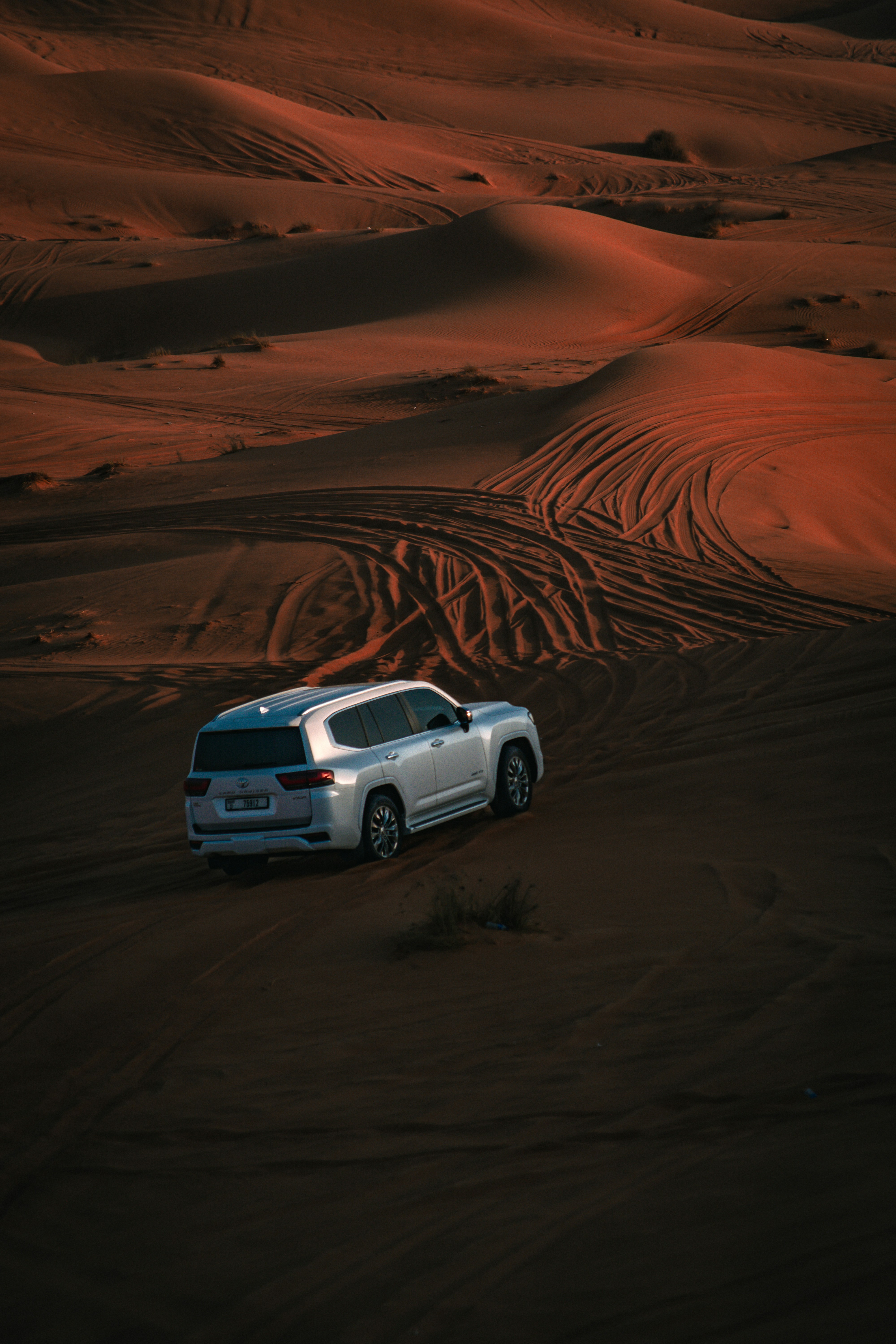 Silver suv driving on sand dunes at sunset