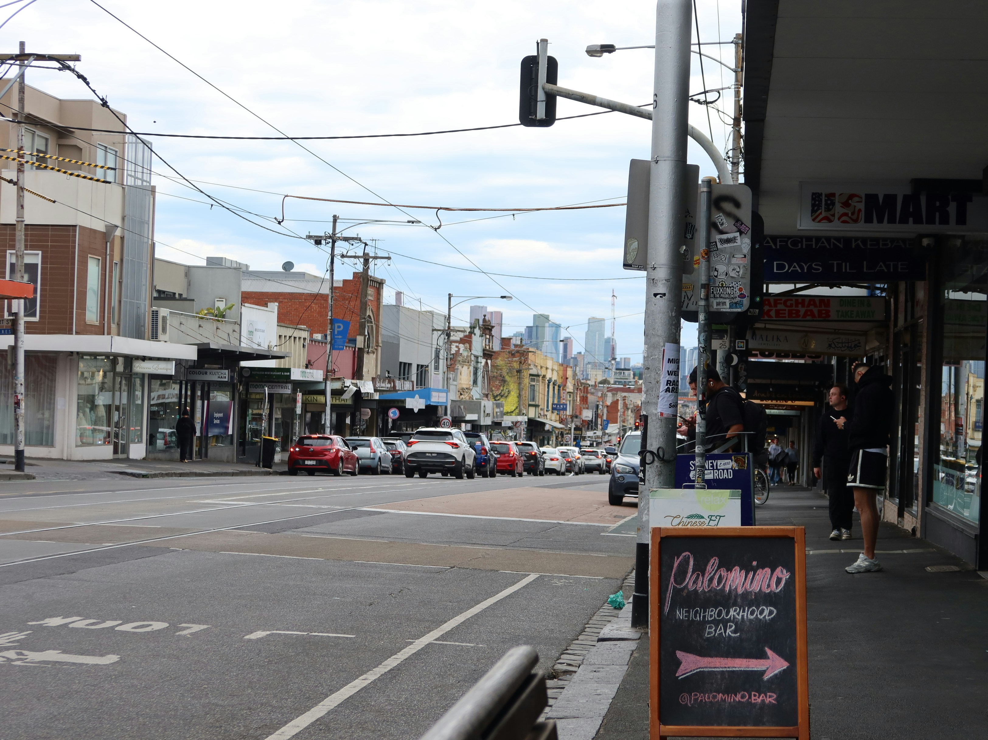 Street view of shops and cars with city skyline.