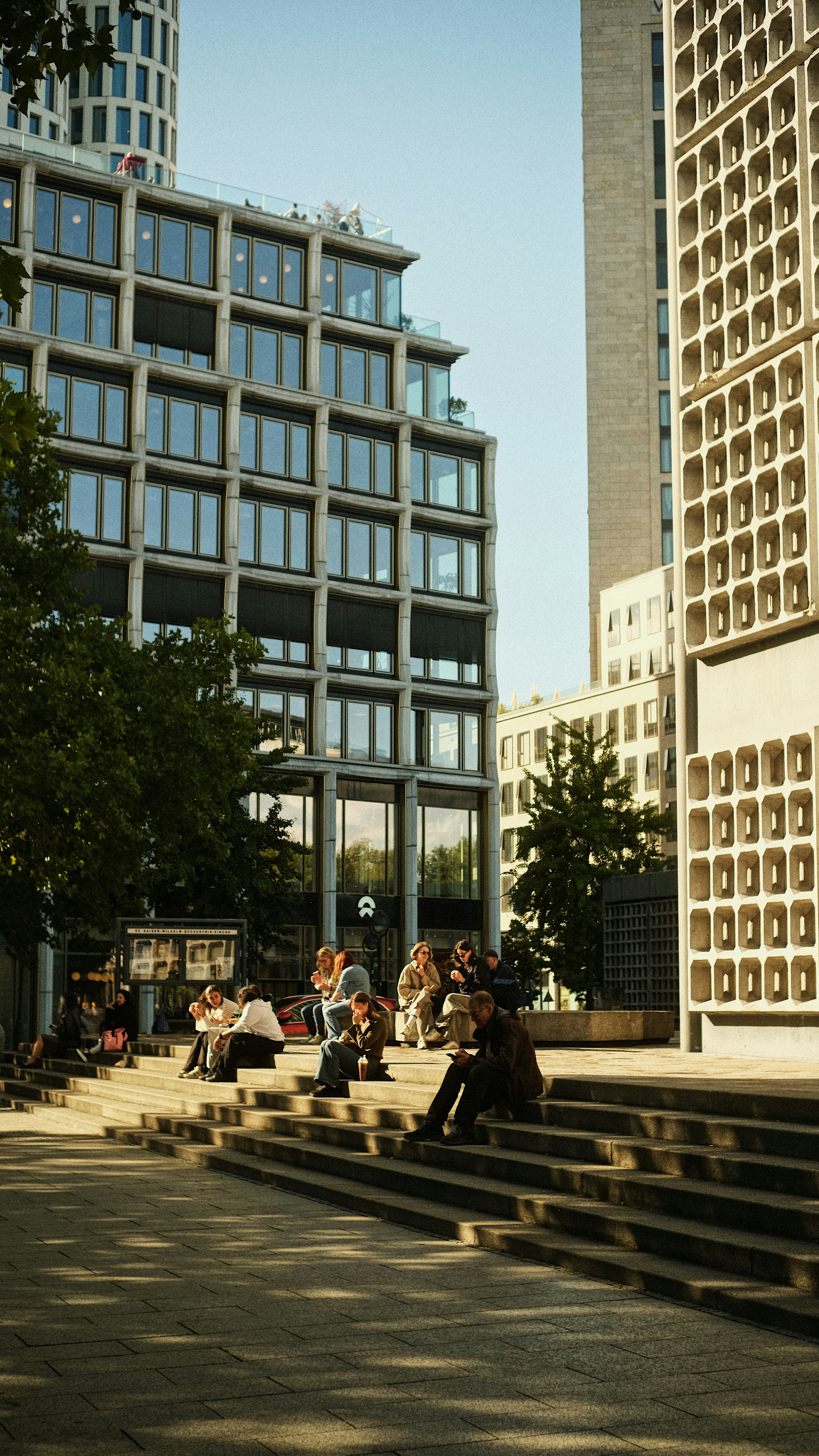 People relaxing on steps in an urban environment, surrounded by modern architecture and greenery.