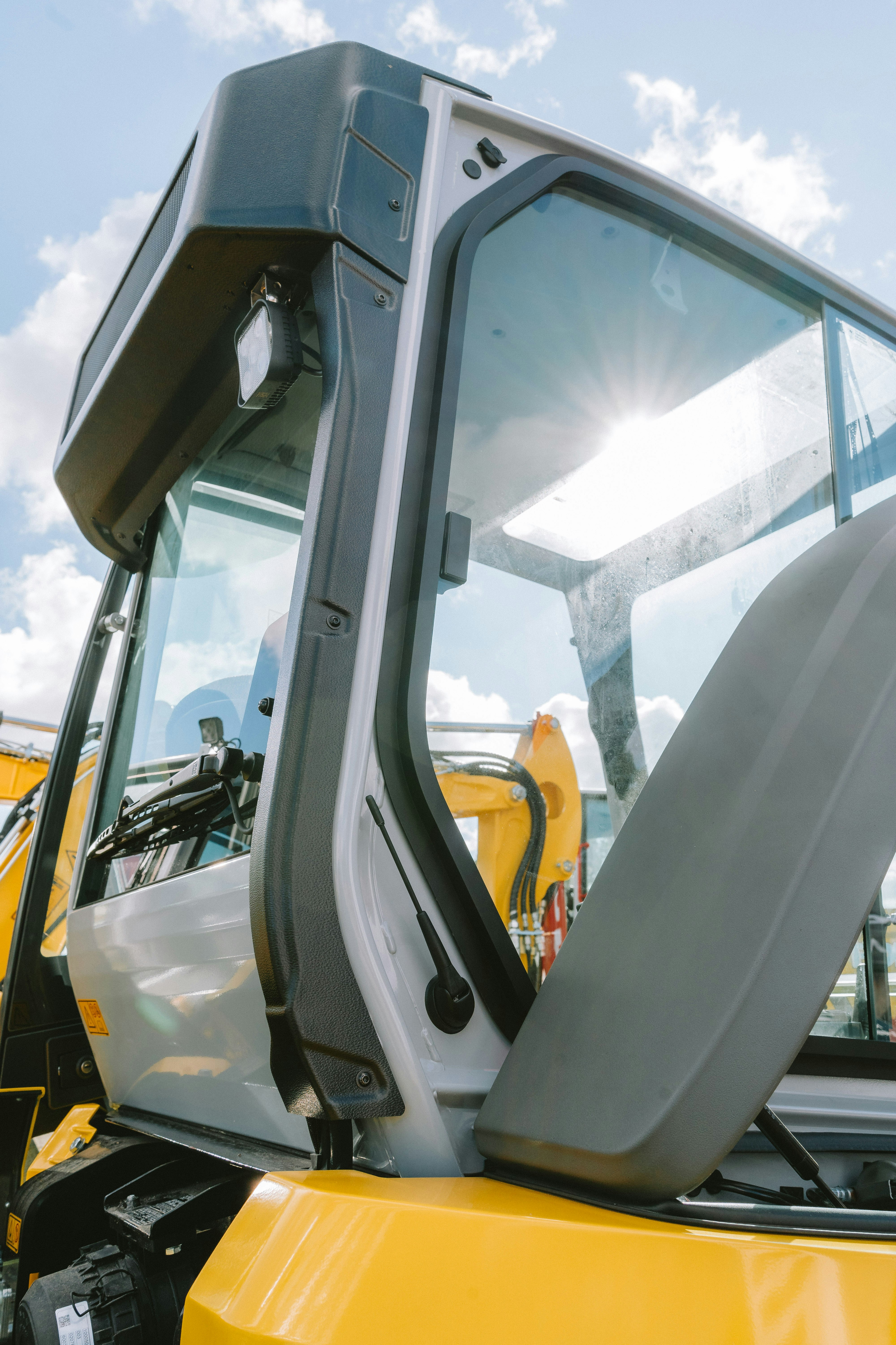 Close-up of a modern construction vehicle's cabin, showcasing its sleek design and operational controls. Sunlight reflects off the glass, adding depth to the scene.