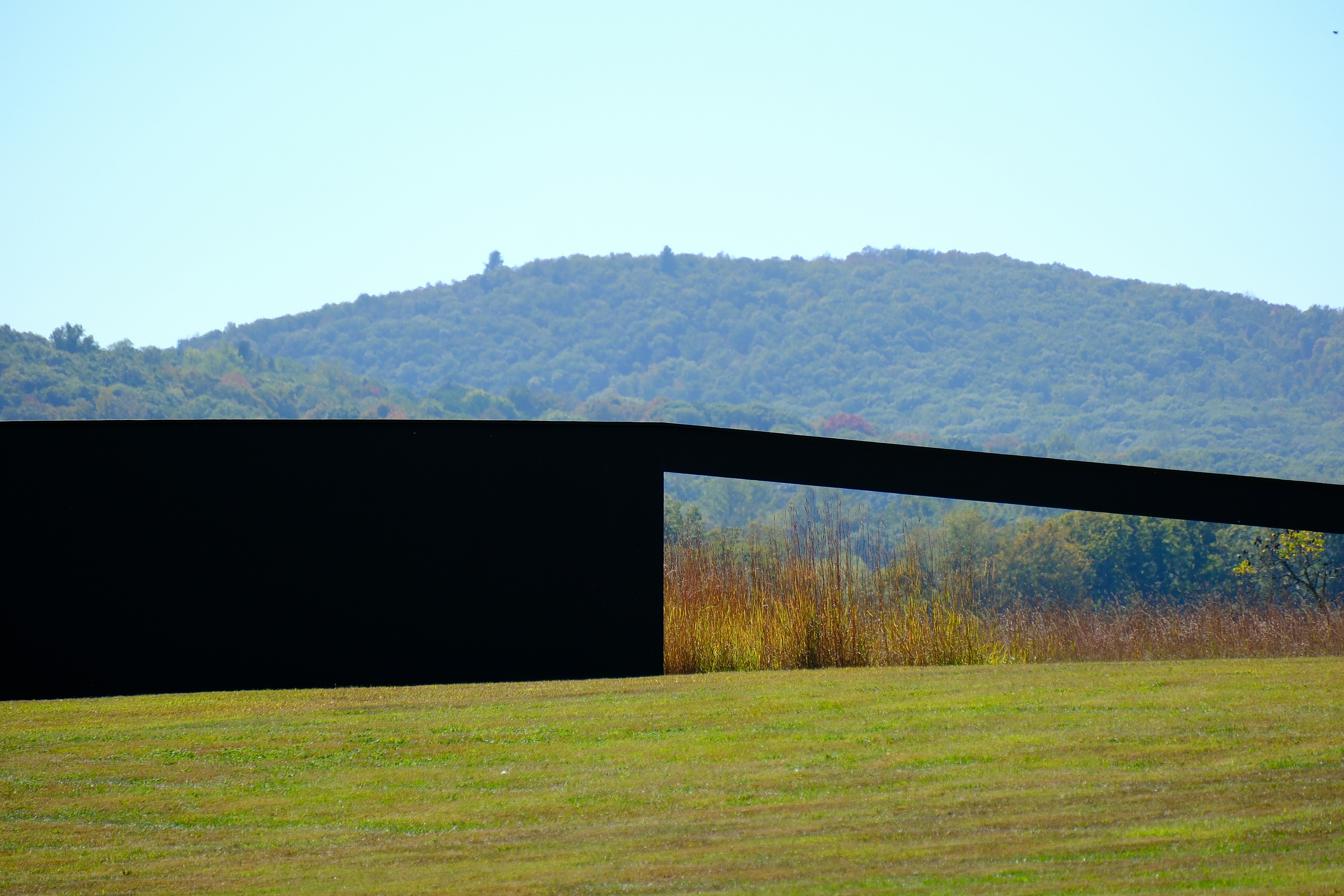 art sculpture on large grassland with mountain in background | Modern black structure in a grassy field.