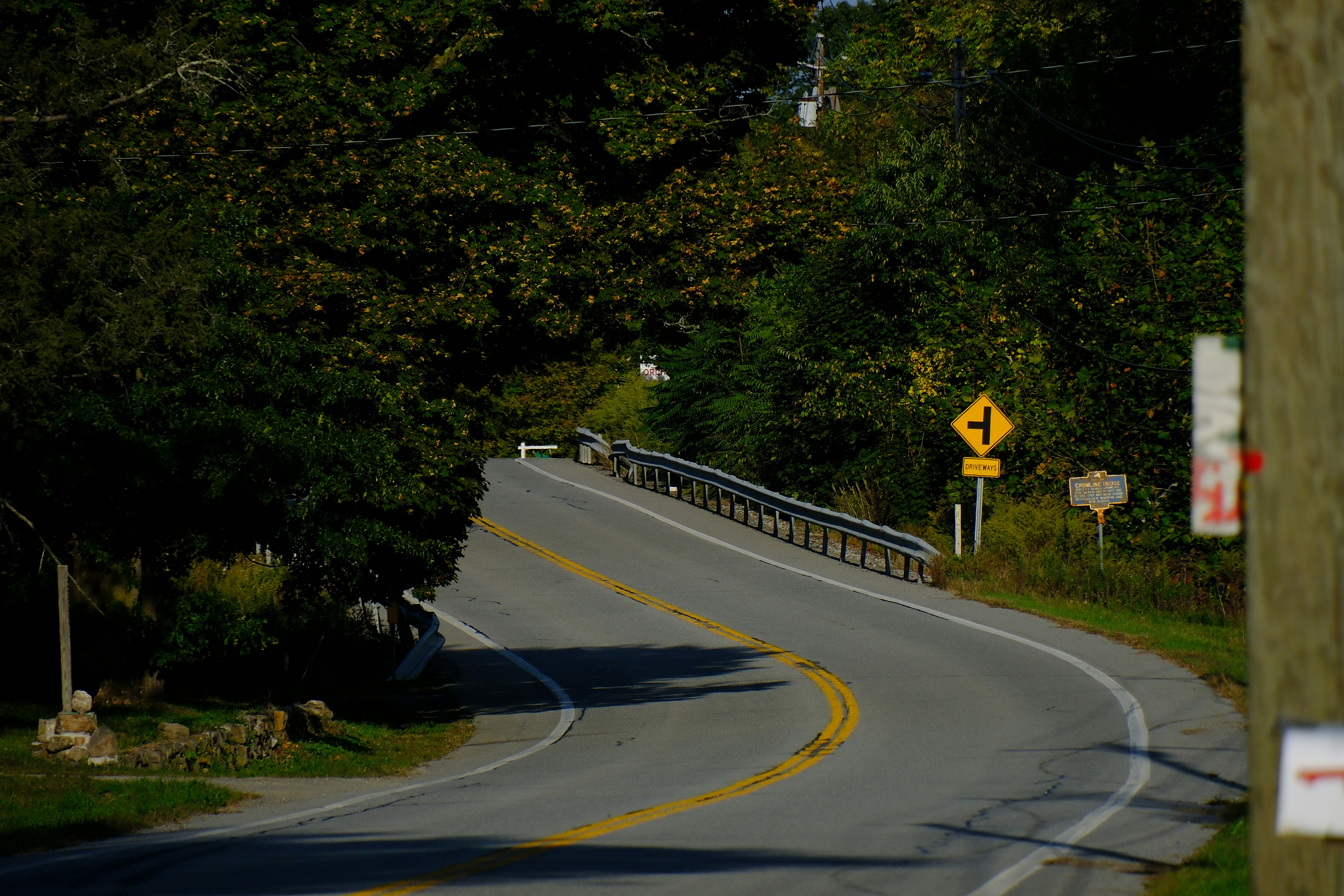 Curving rural road flanked by lush greenery and directional signage, inviting exploration. A tranquil scene highlighting the beauty of rural landscapes.