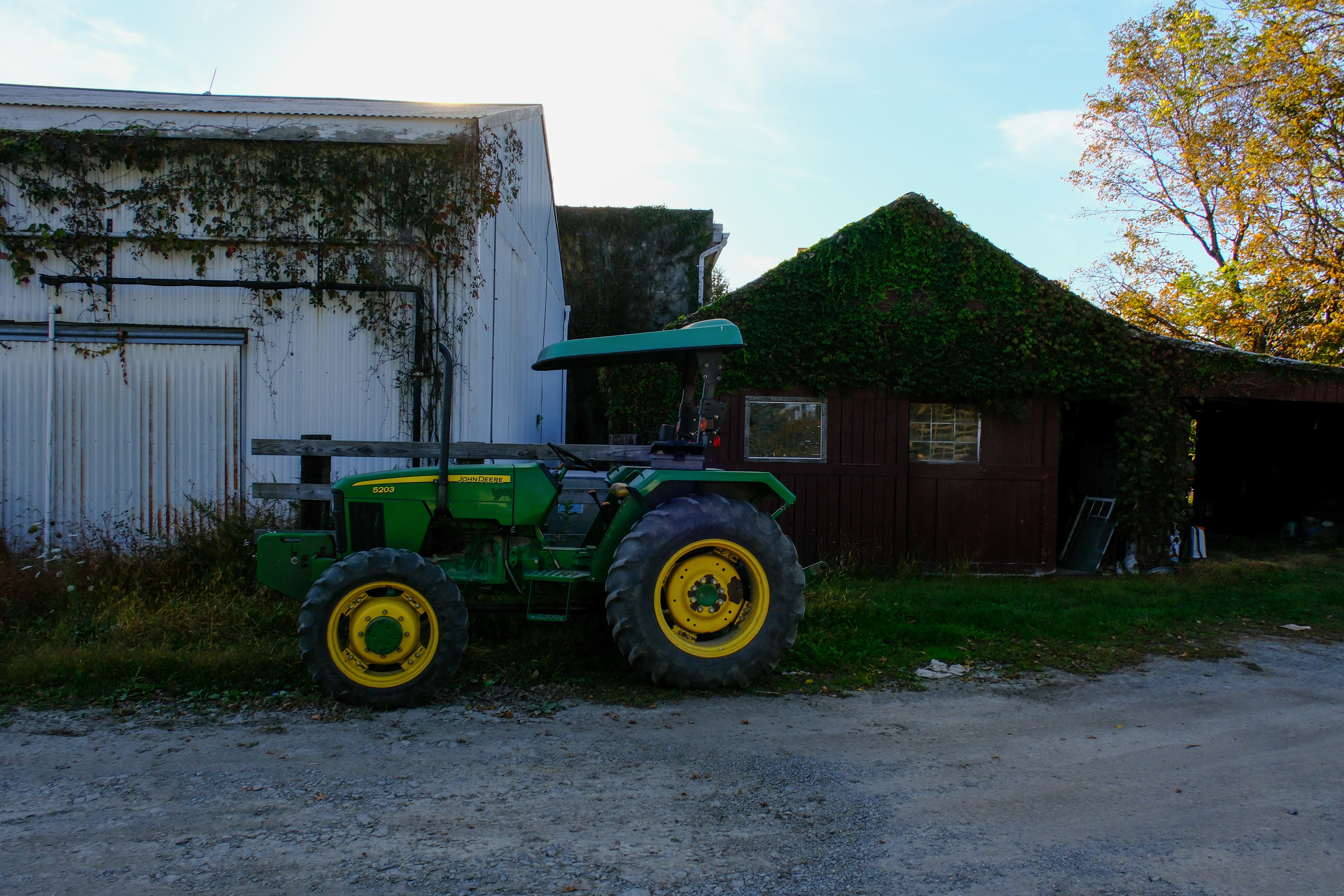 Green tractor parked beside old farm buildings