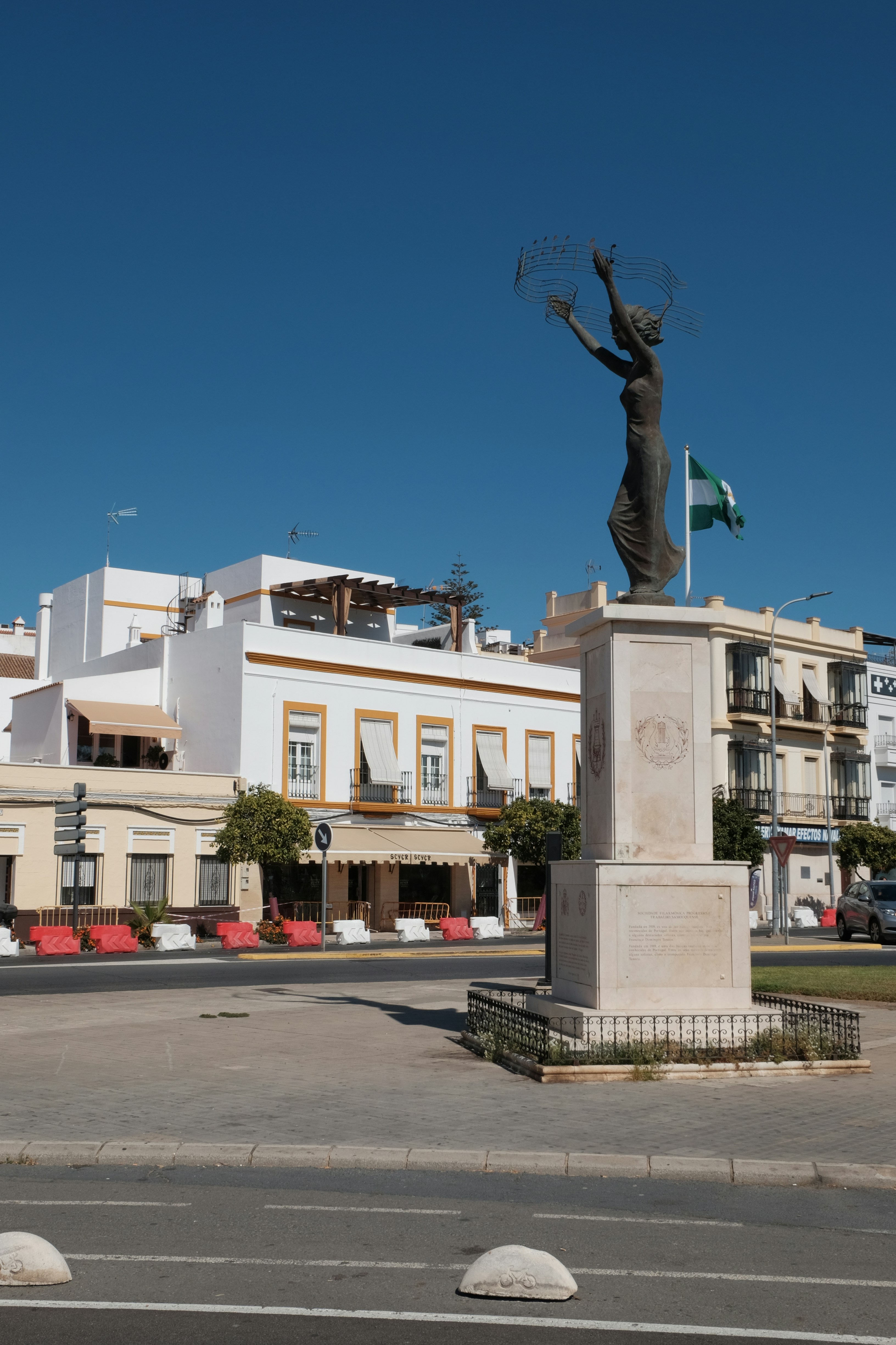 Statue in a town square with buildings and flag.