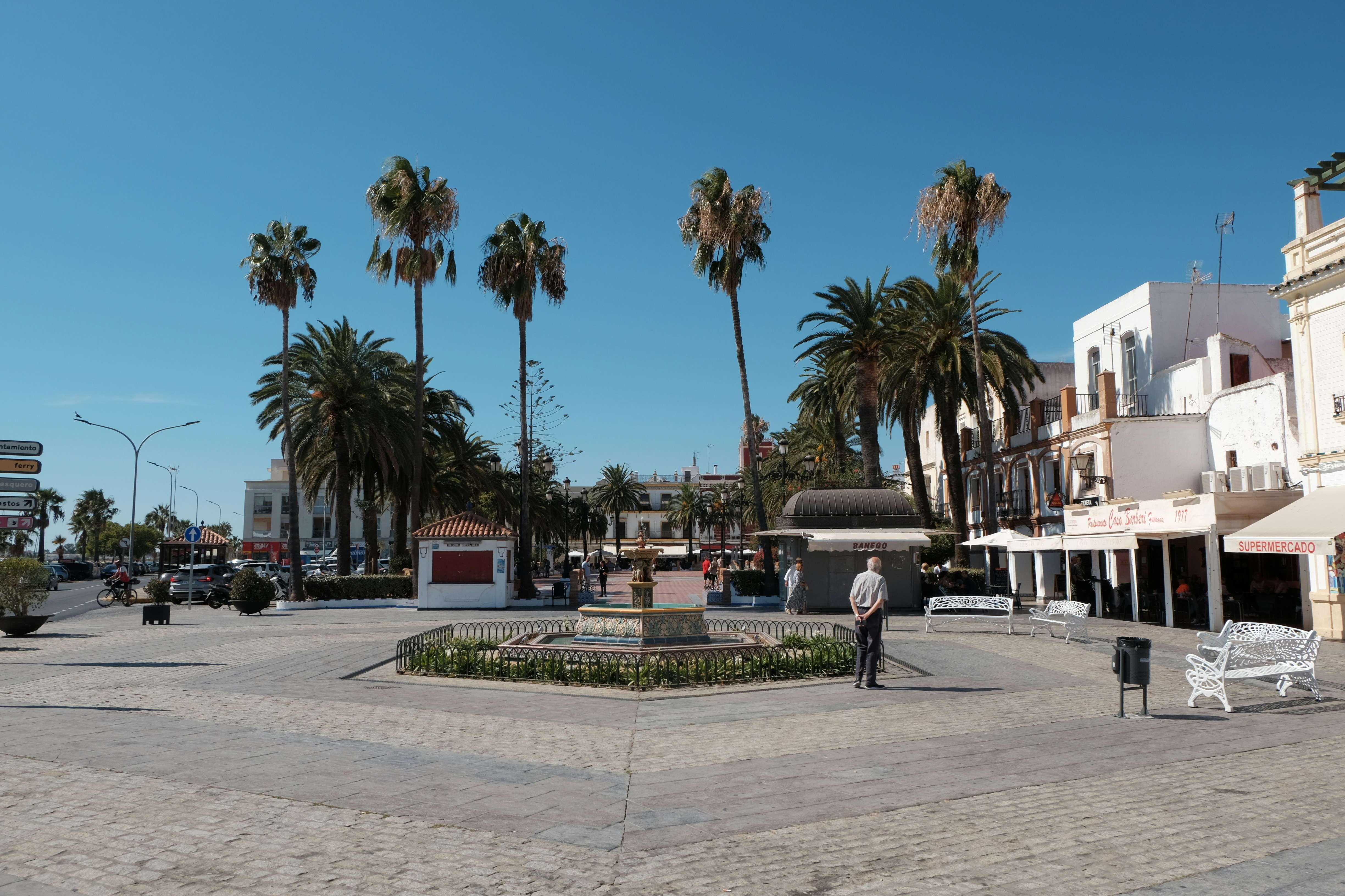 Man walking in a sunny town square with palm trees