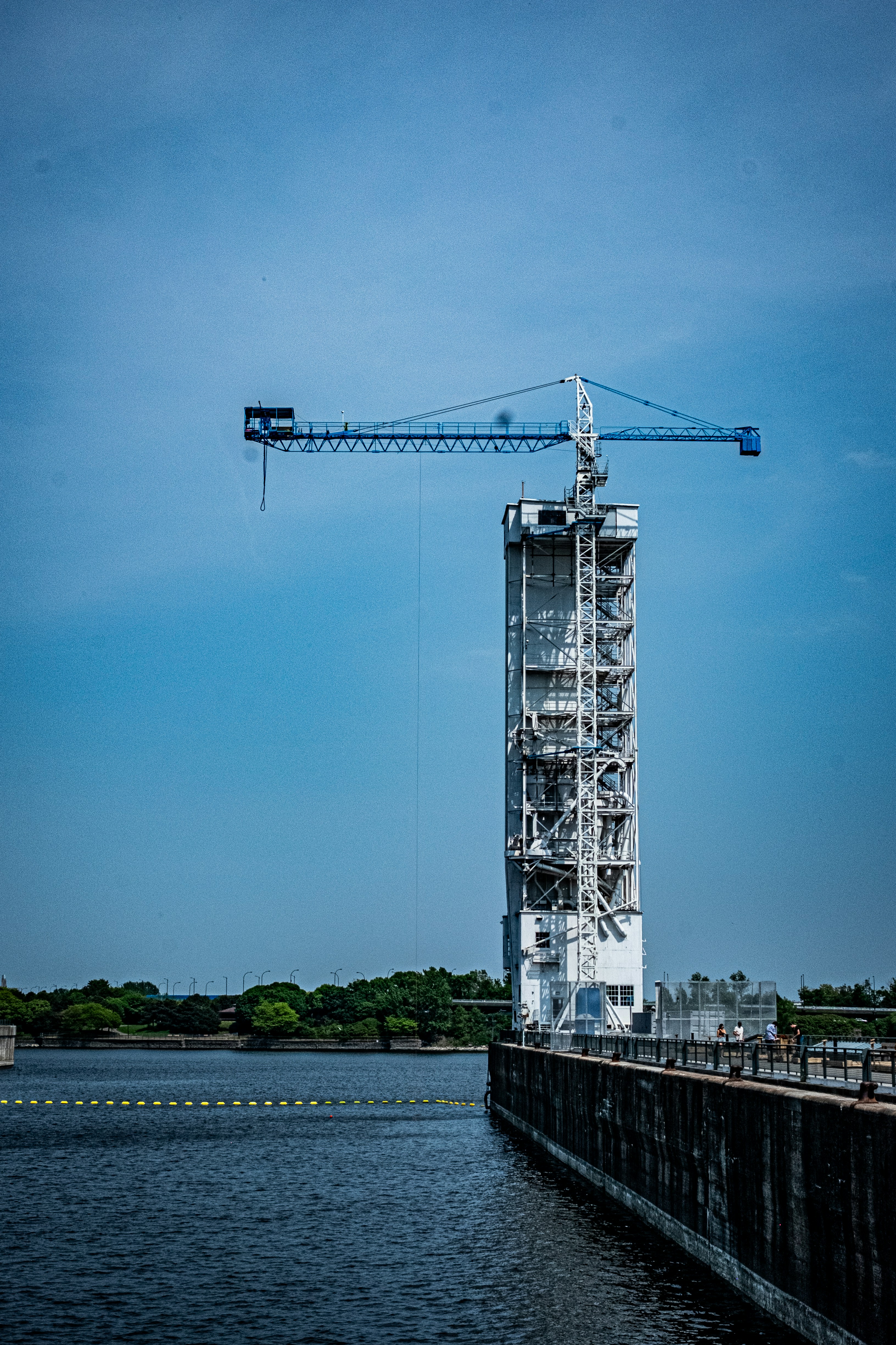 A tall industrial tower with a crane above water.