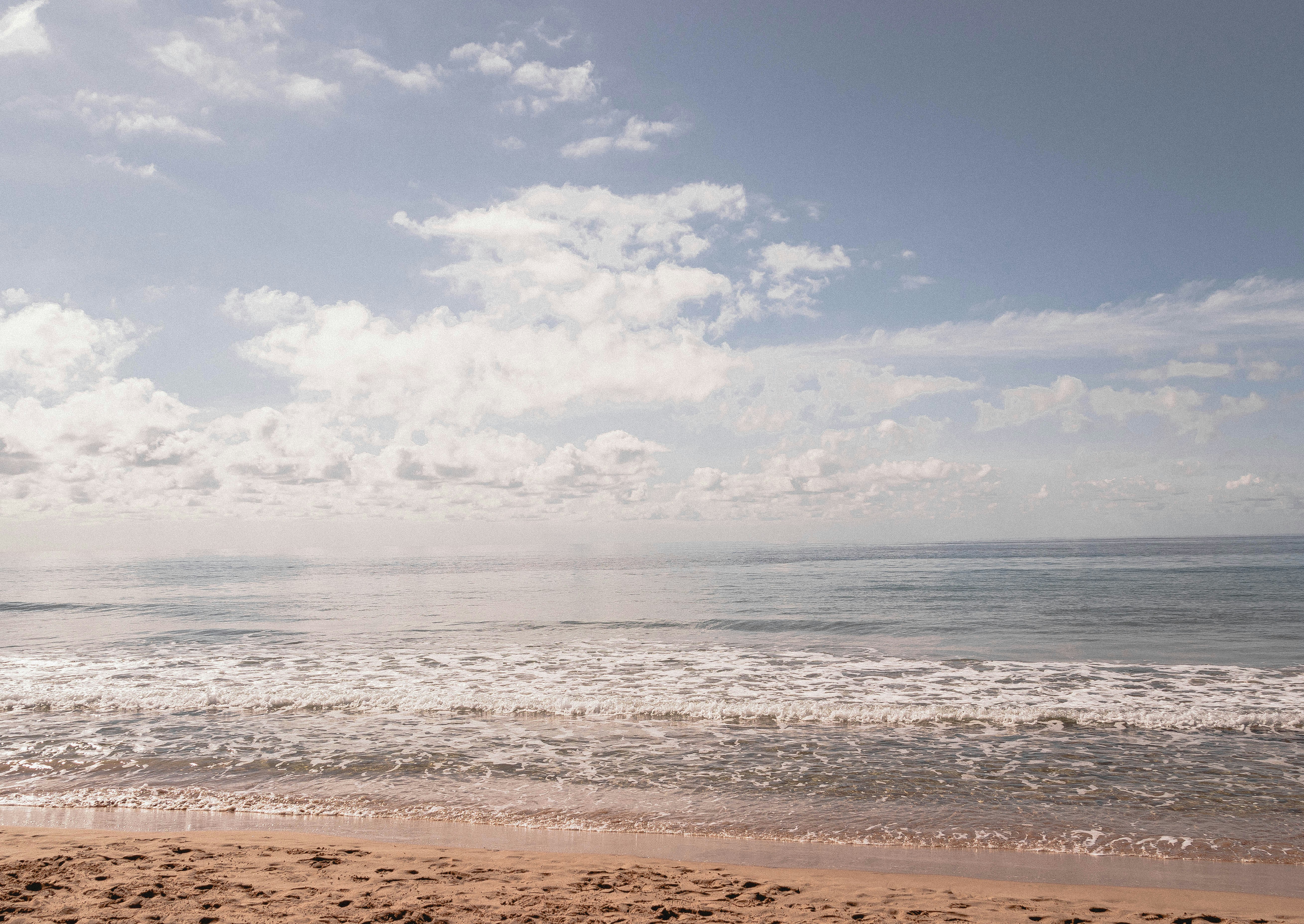 Gentle waves lap a sandy beach under a cloudy sky.
