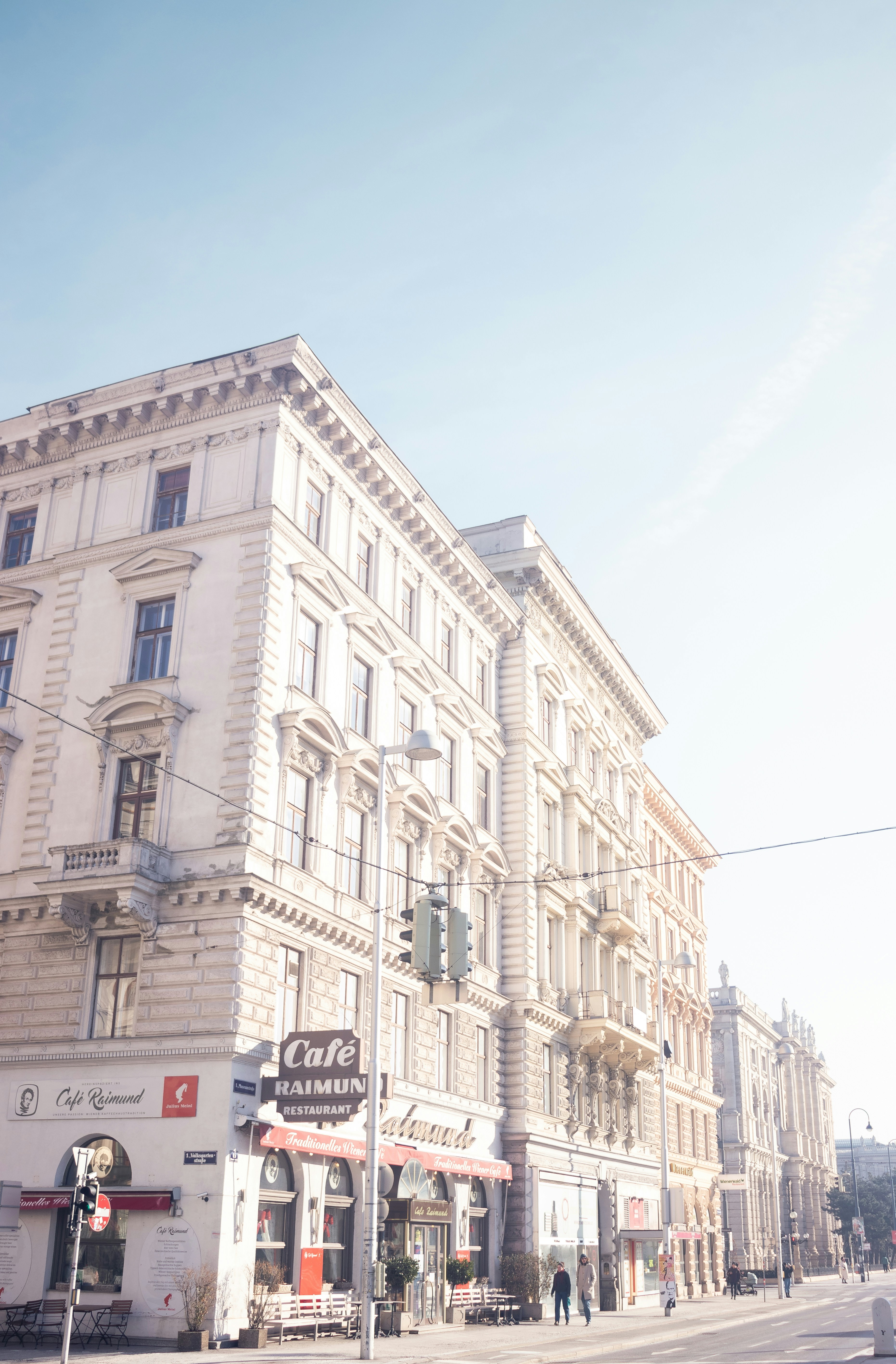 Historic buildings with intricate architectural details line a bustling street, showcasing the charm of urban life. The scene is bathed in soft morning light.