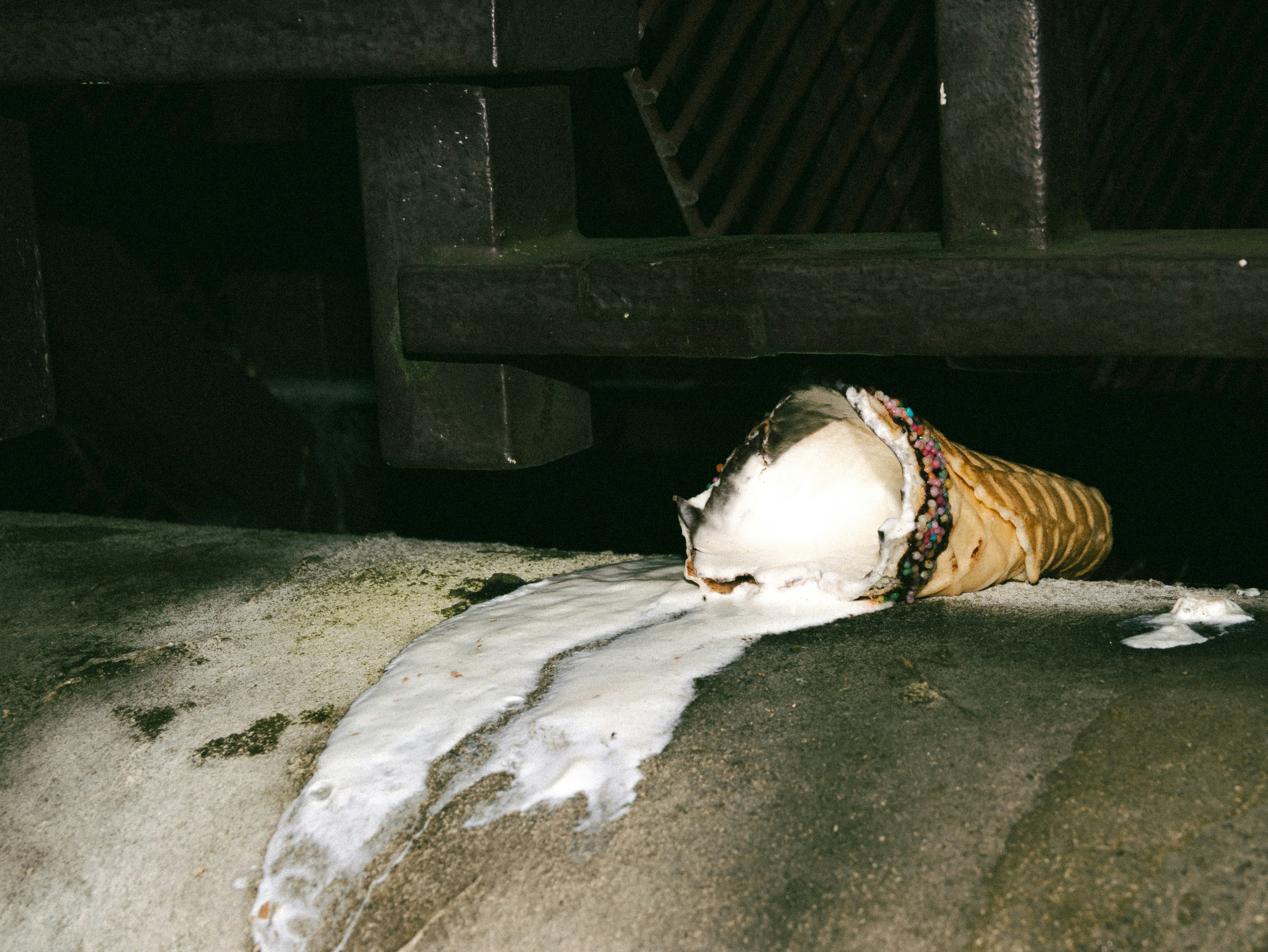 Ice cream cone toppled over, spilling its contents onto a textured surface. The scene captures the fleeting nature of indulgence.