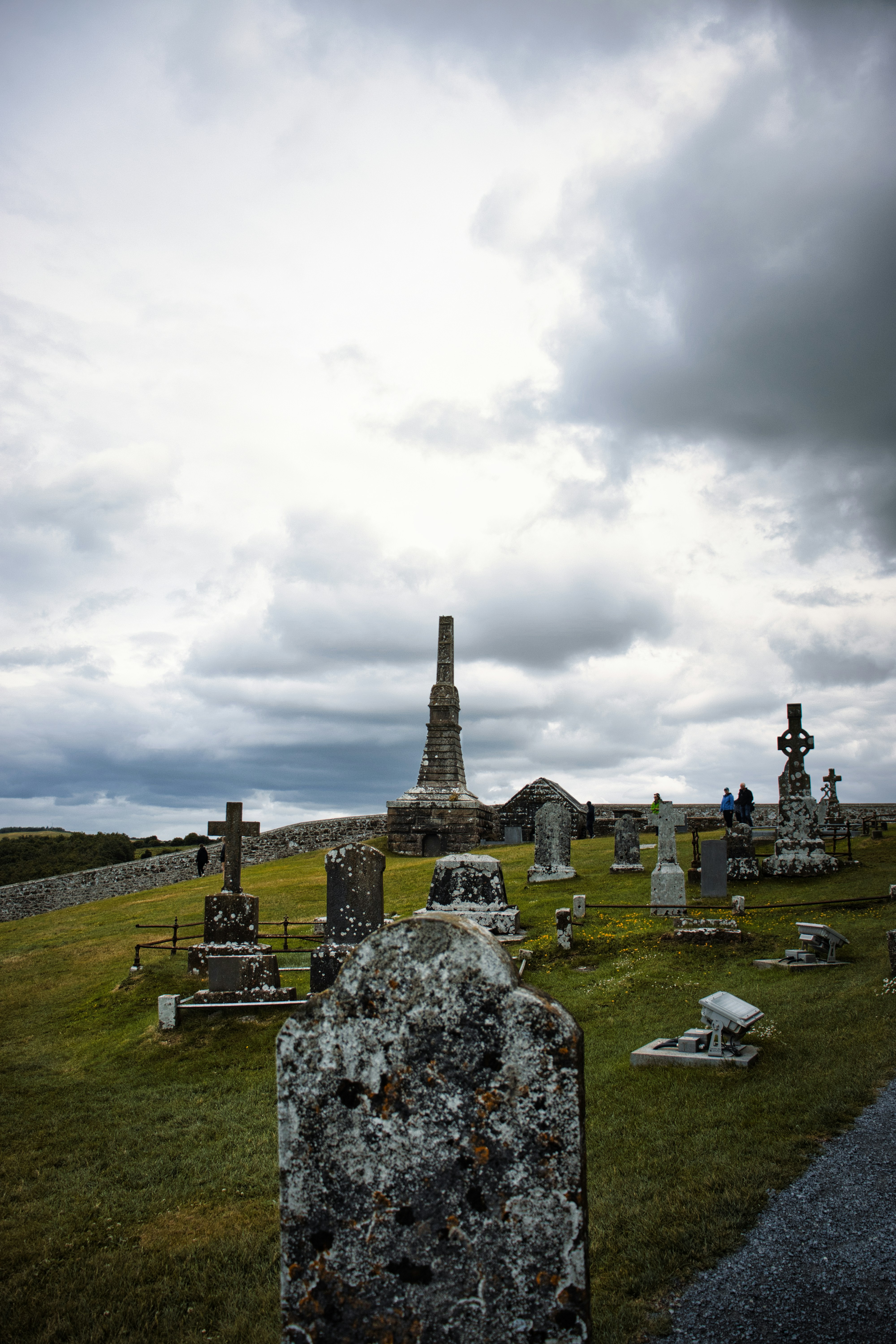 Historic graveyard with weathered tombstones and a prominent monument under a dramatic sky. The scene evokes a sense of reflection and remembrance.