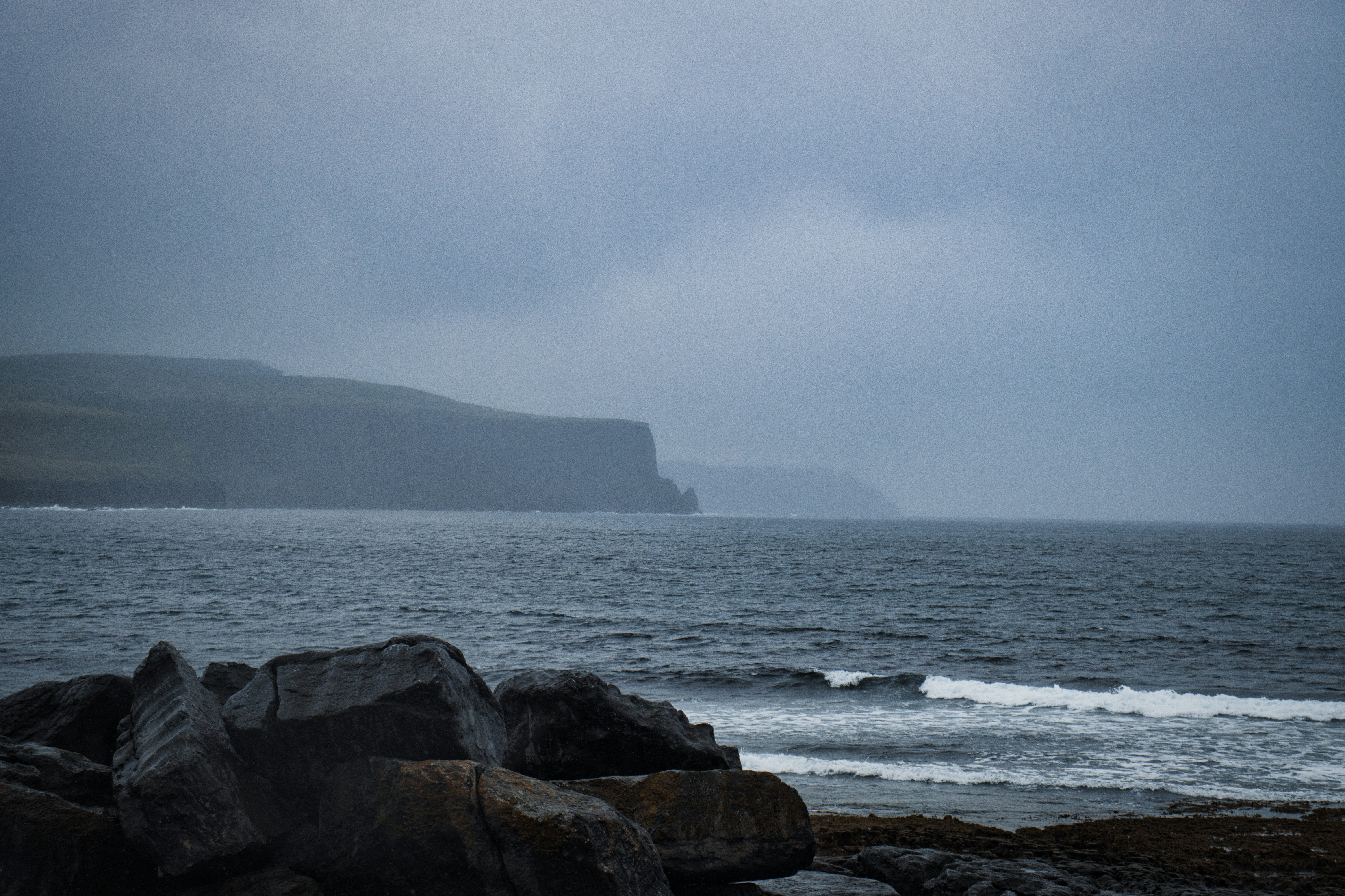 Misty cliffs overlook a choppy ocean on a cloudy day.