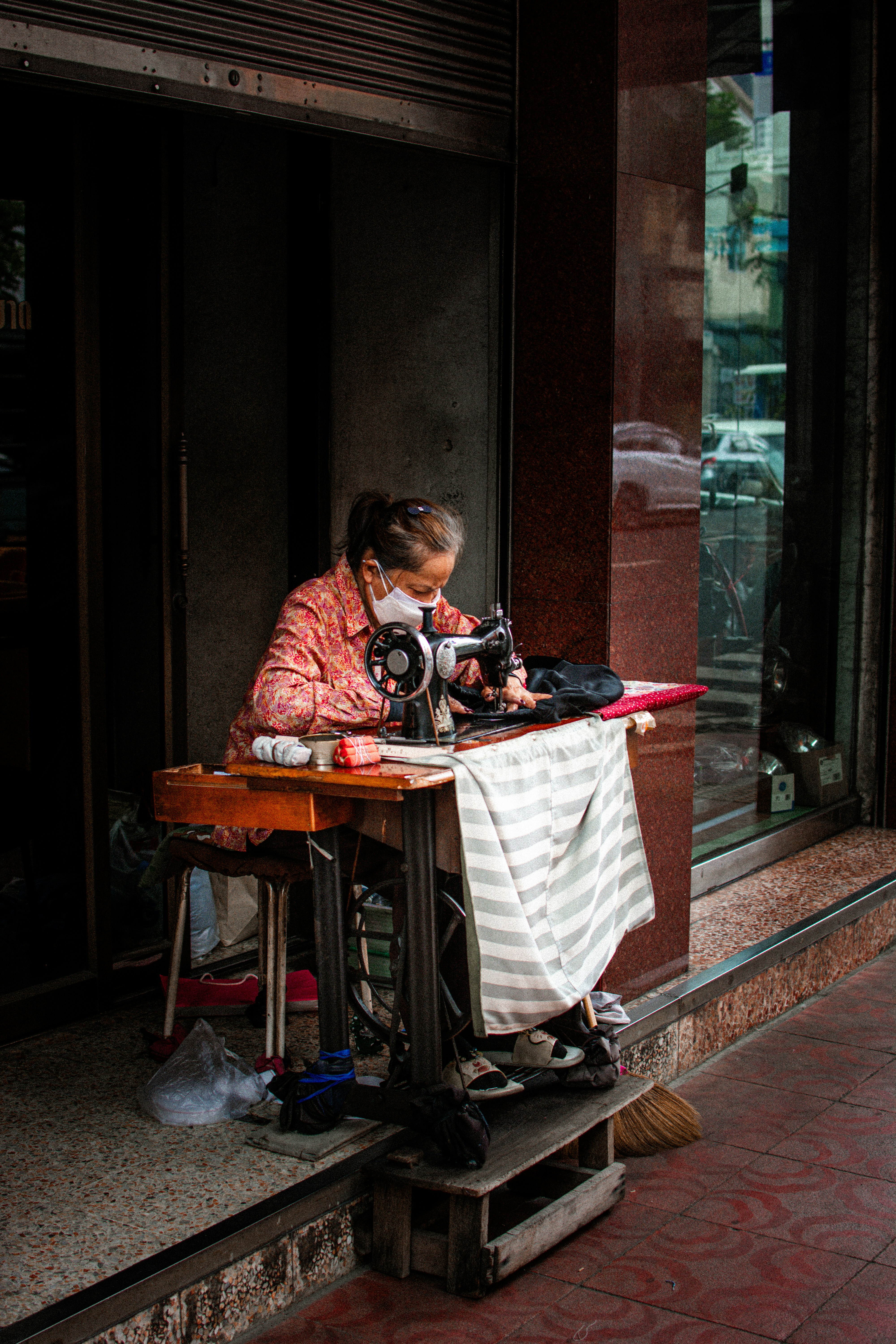 Woman wearing mask sewing on vintage machine outdoors.