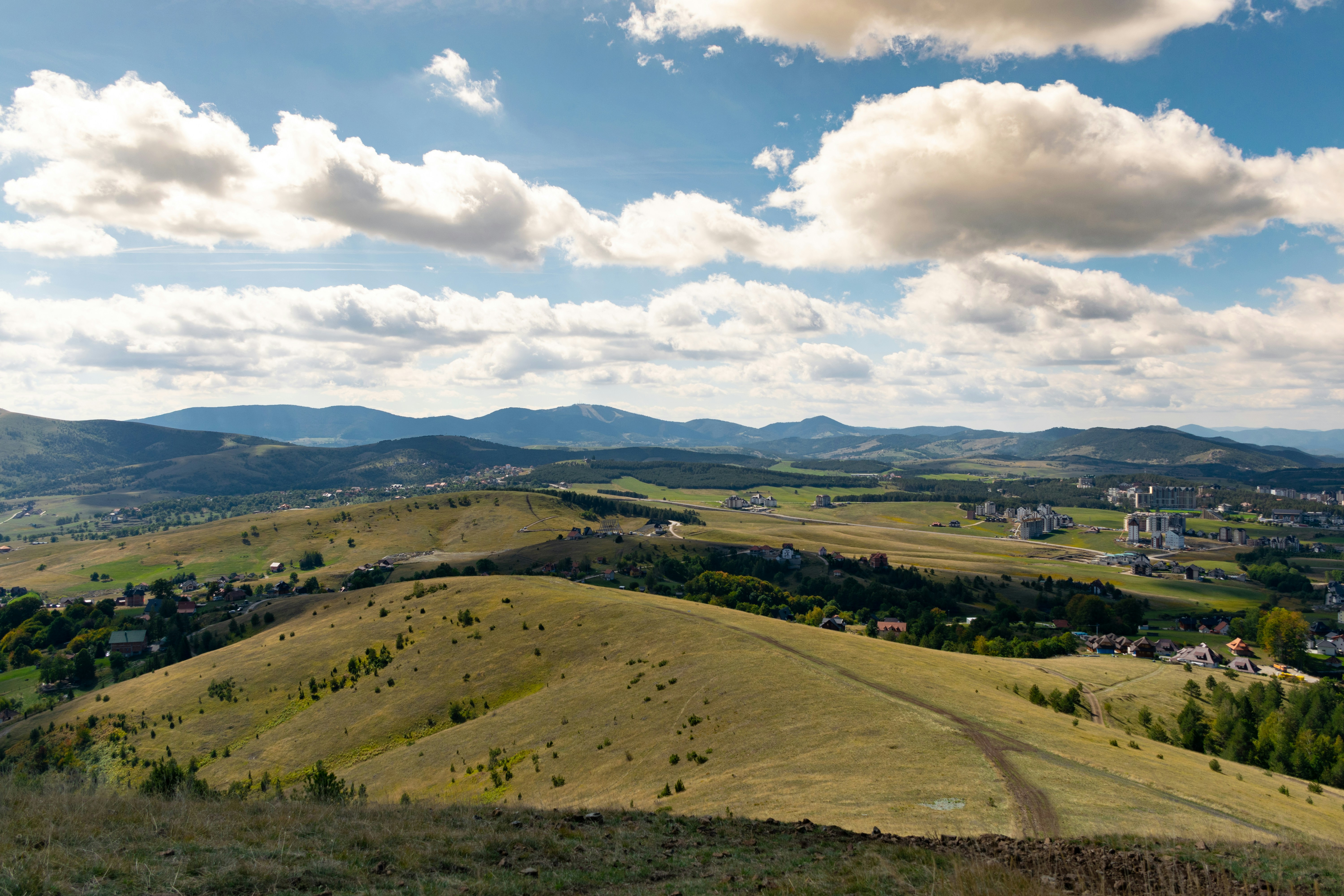 Vast landscape showcasing rolling hills and distant mountains under a dynamic sky filled with clouds. The scene captures the tranquility of rural life.