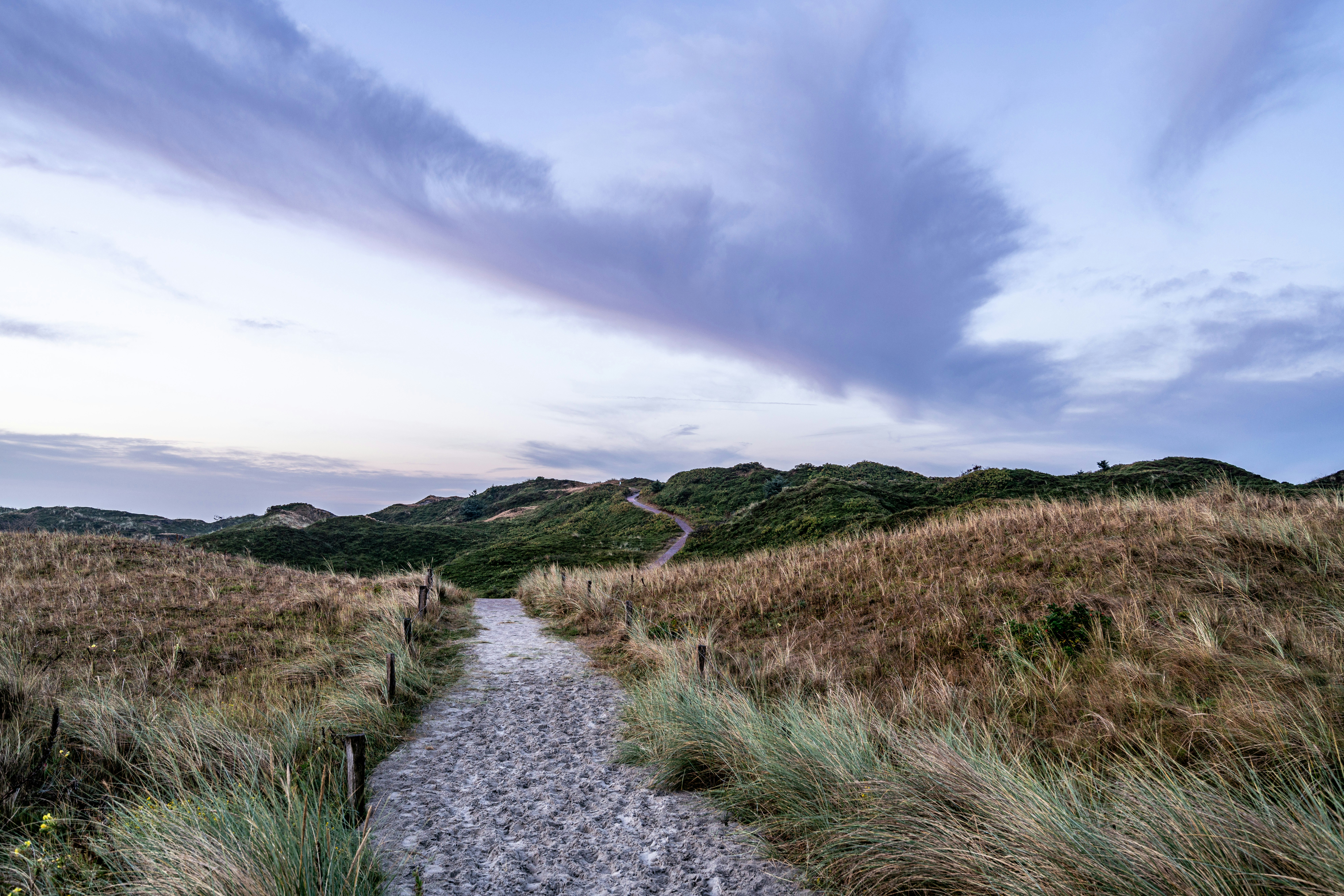 Sandy path through grassy dunes under a cloudy sky