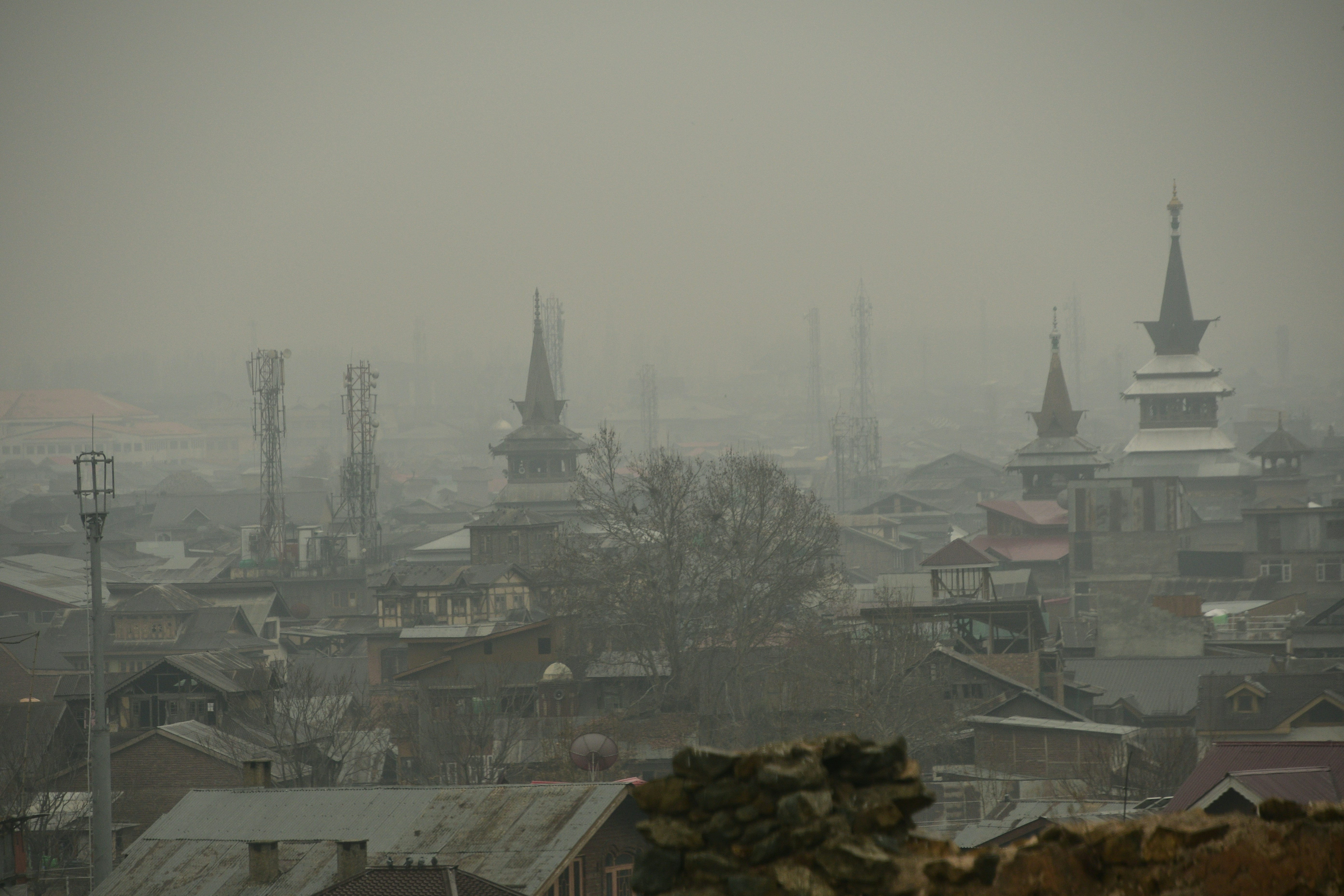 A foggy cityscape featuring traditional spires and rooftops, partially obscured by atmospheric haze. The scene conveys a sense of mystery and tranquility.